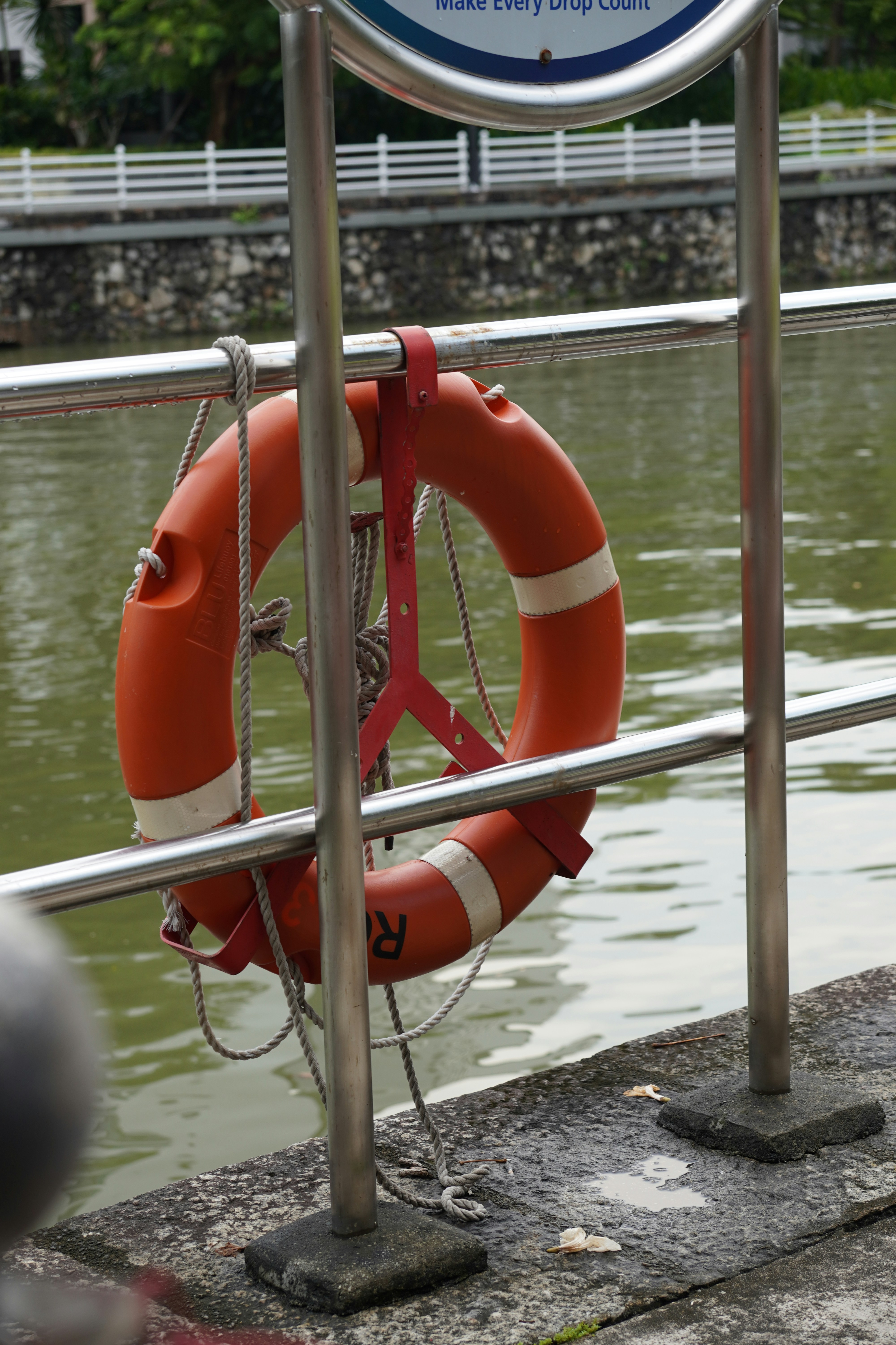 Orange Lifebuoy Framed by Chrome Railings Along a Riverside Path