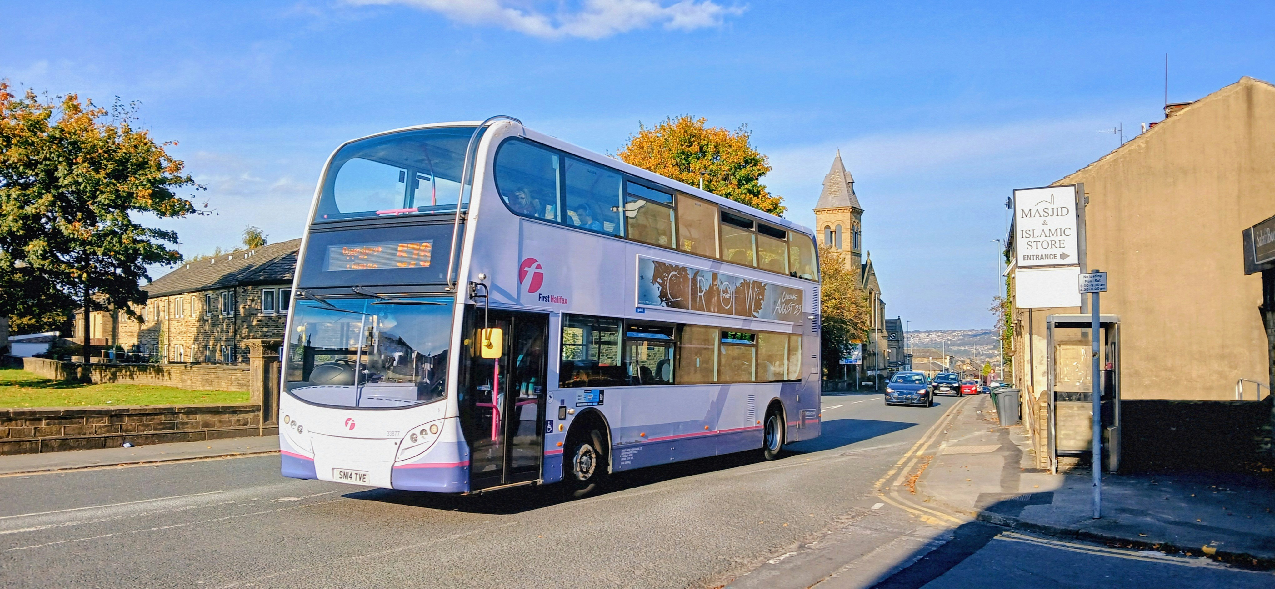 Pastel Purple-White Double-Decker Navigates a Sunlit Town Street