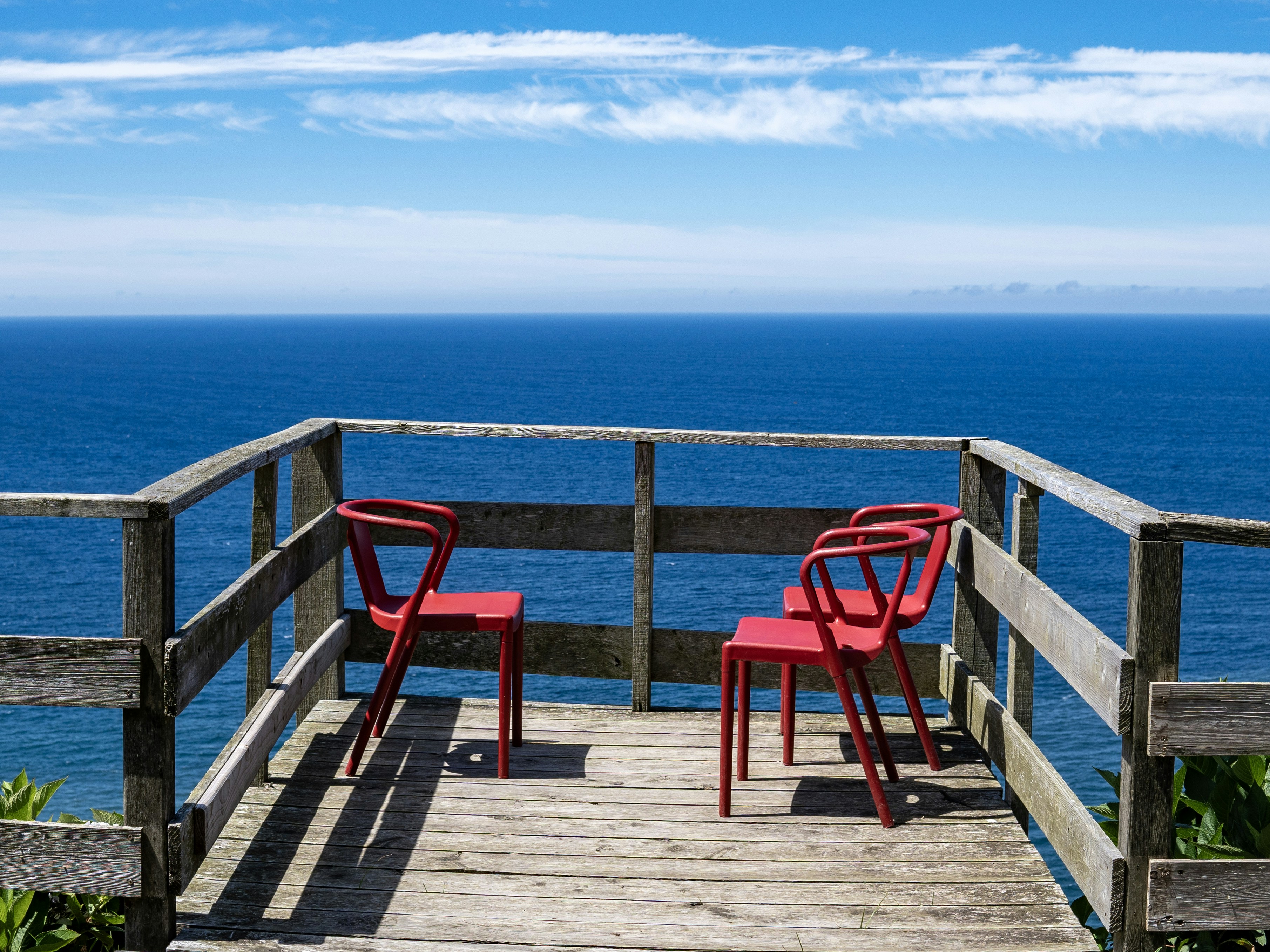 Two Crimson Chairs on a Weathered Deck Over an Endless Blue Expanse