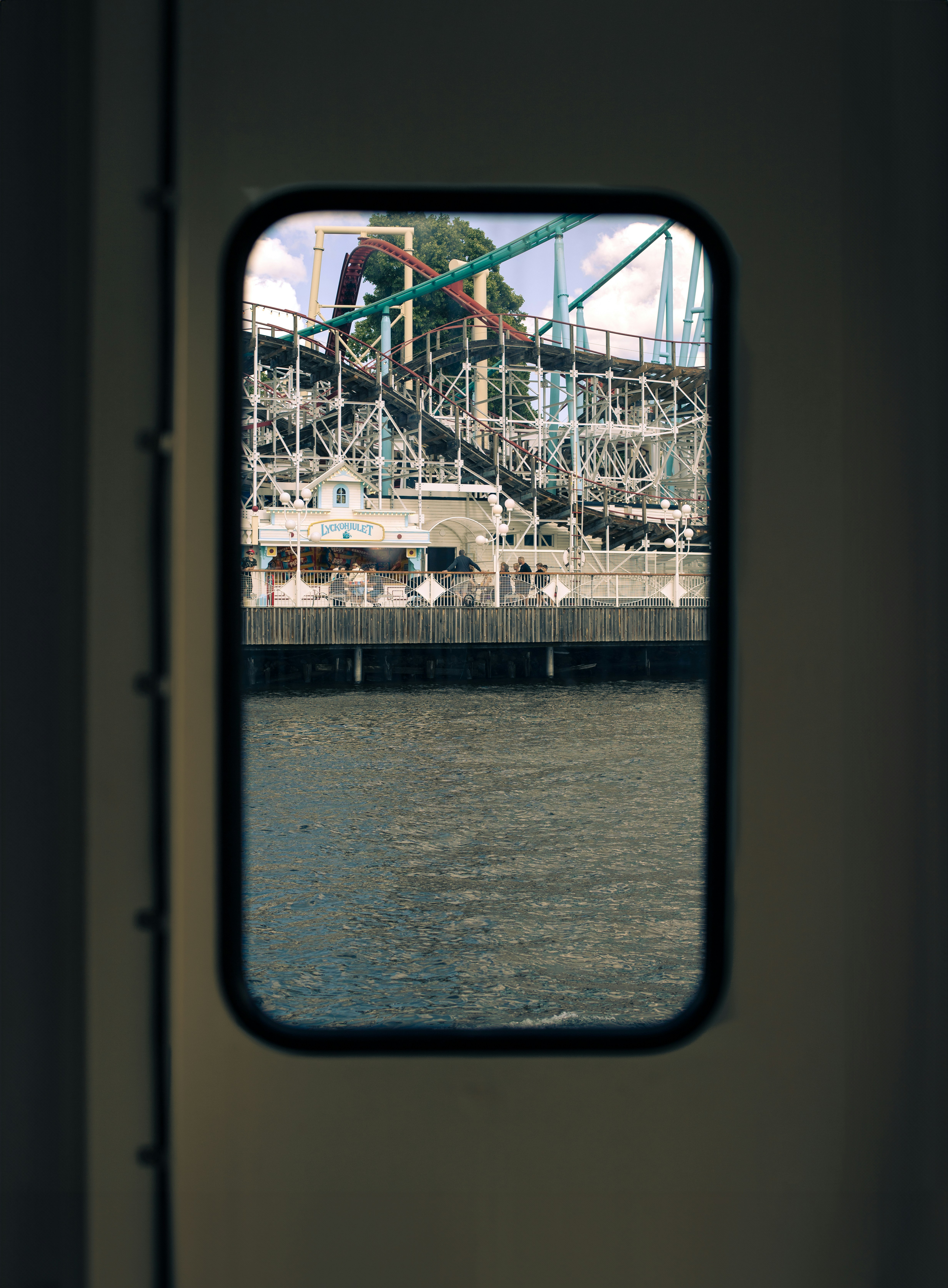 Portside Pulse: Pier-Top Roller Coaster Framed by a Ship's Window