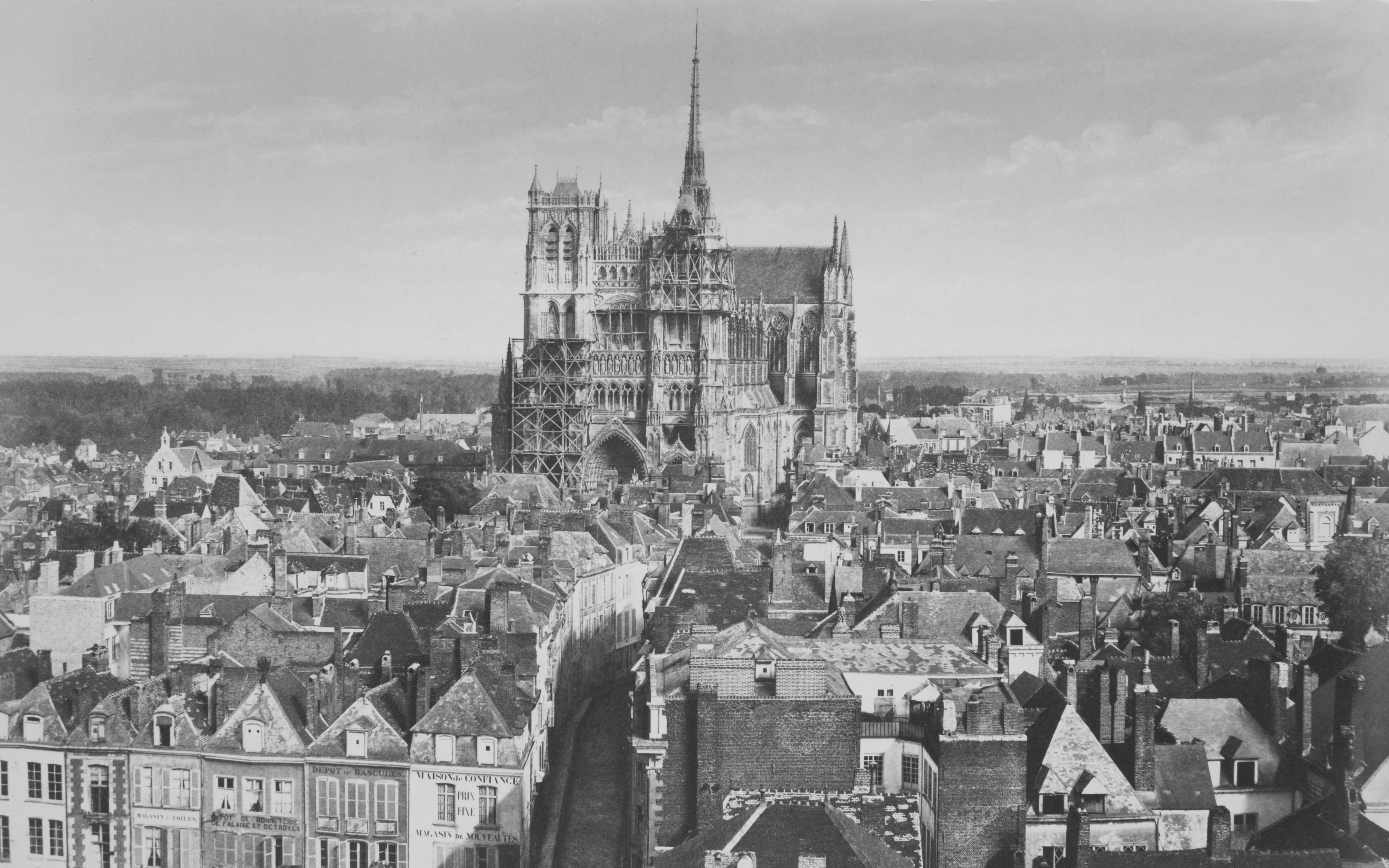 Black and white photograph of a grand cathedral towering over a dense cityscape of rooftops.