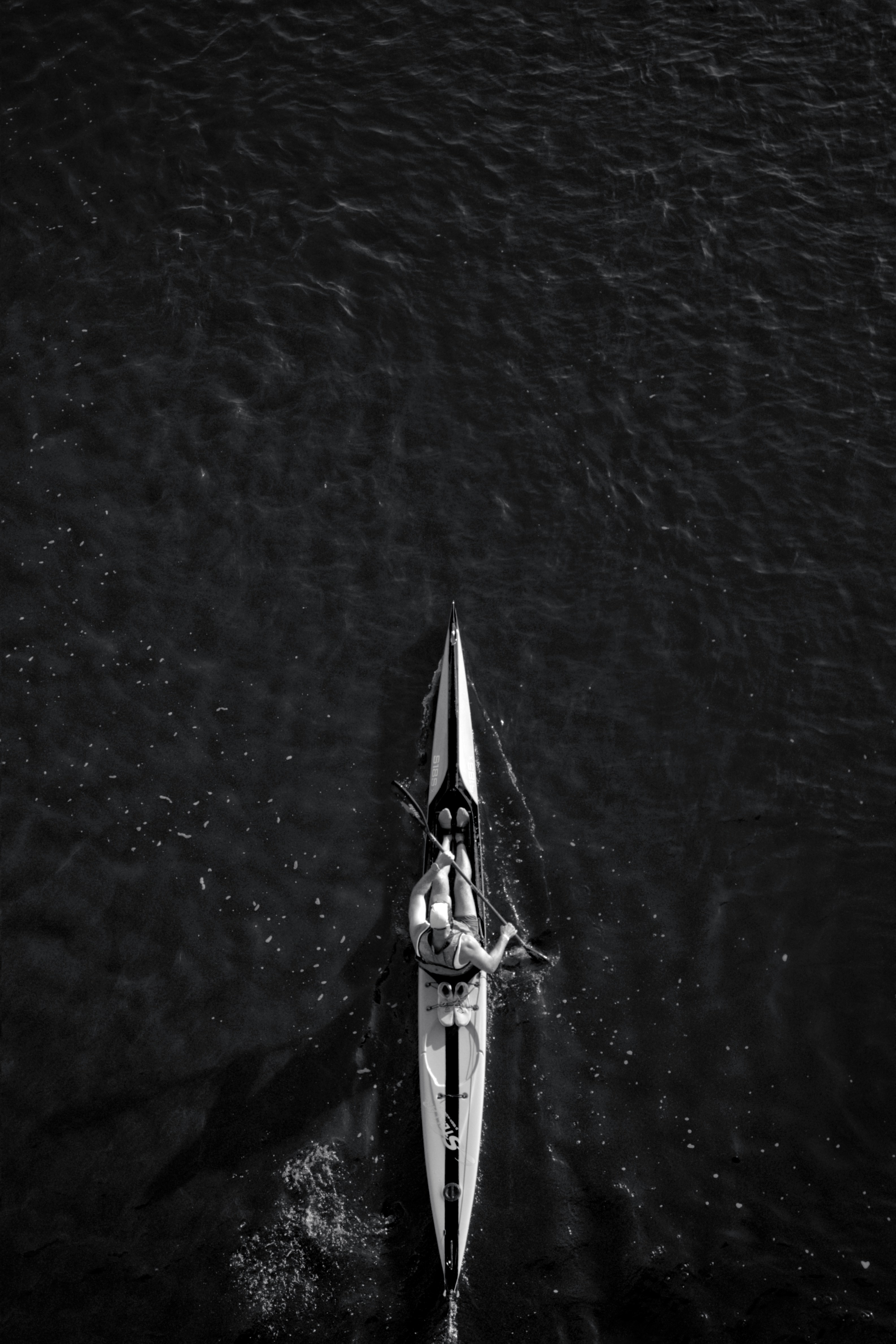 Aerial Glide: lone rower in a slender shell on midnight water