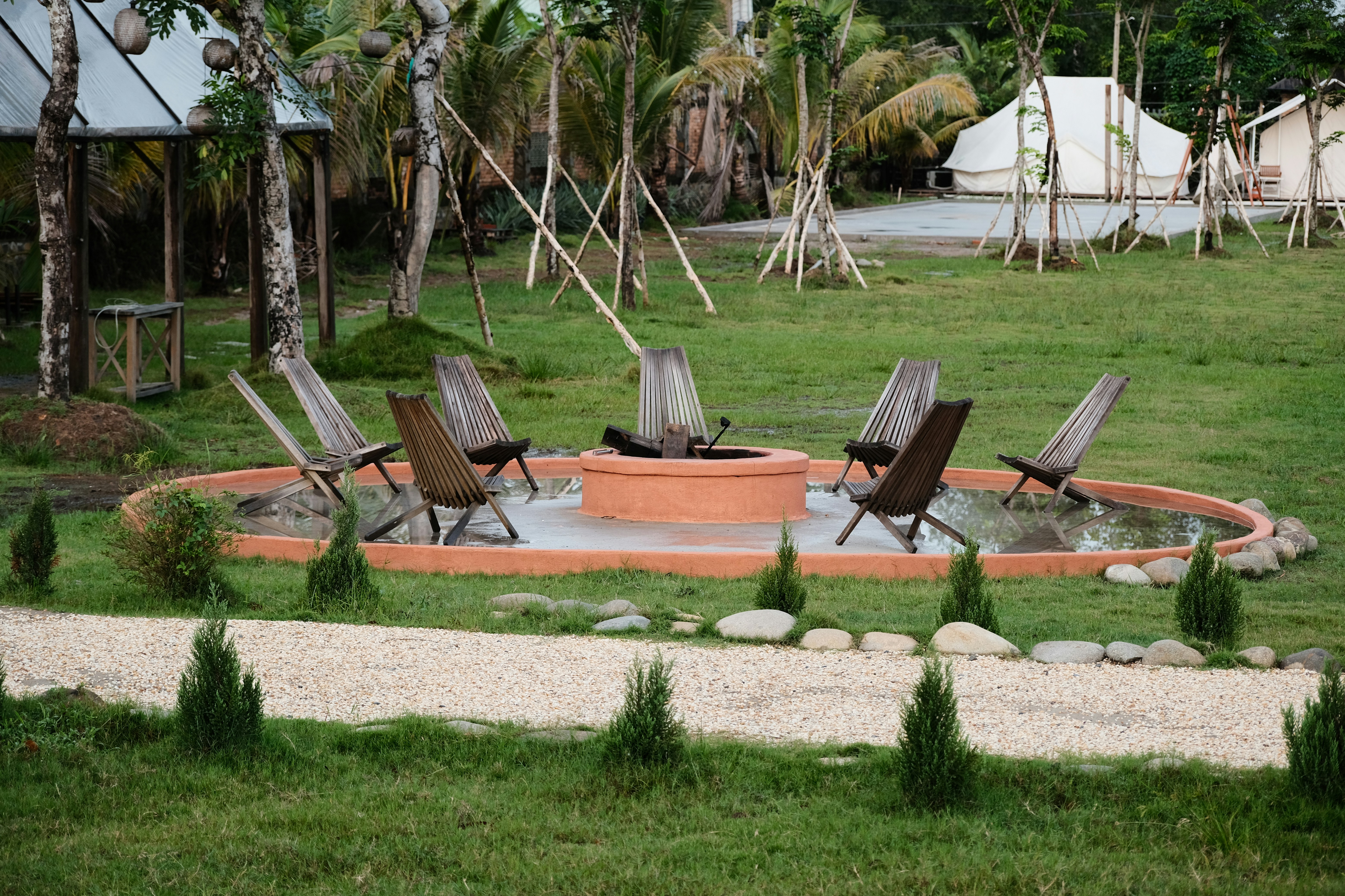 Circular Fire Pit Ensemble Framed by Wooden Lounge Chairs in a Tropical Resort Garden