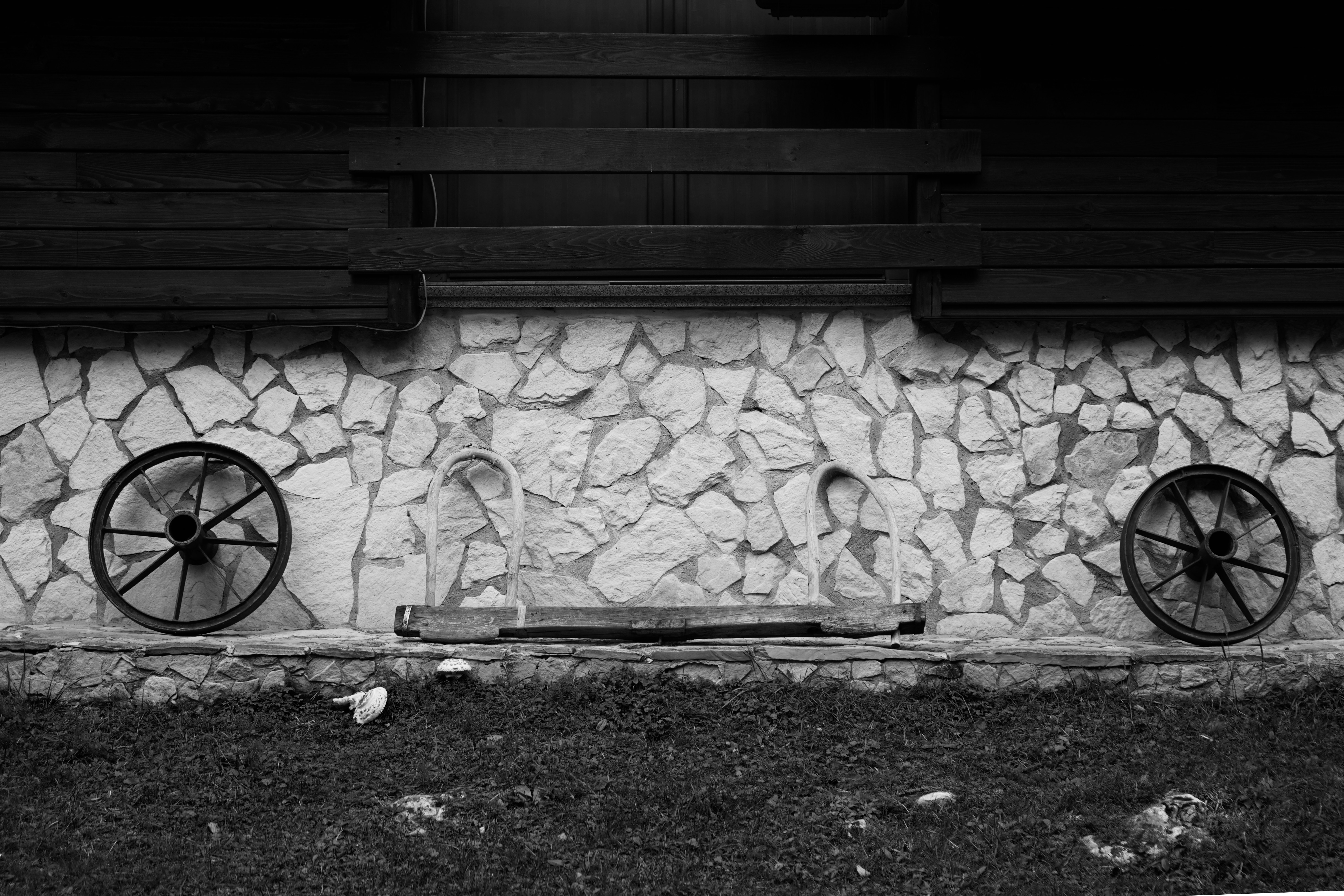 Stone Wall Echoes: Wagon Wheels Framing a Quiet Monochrome Moment