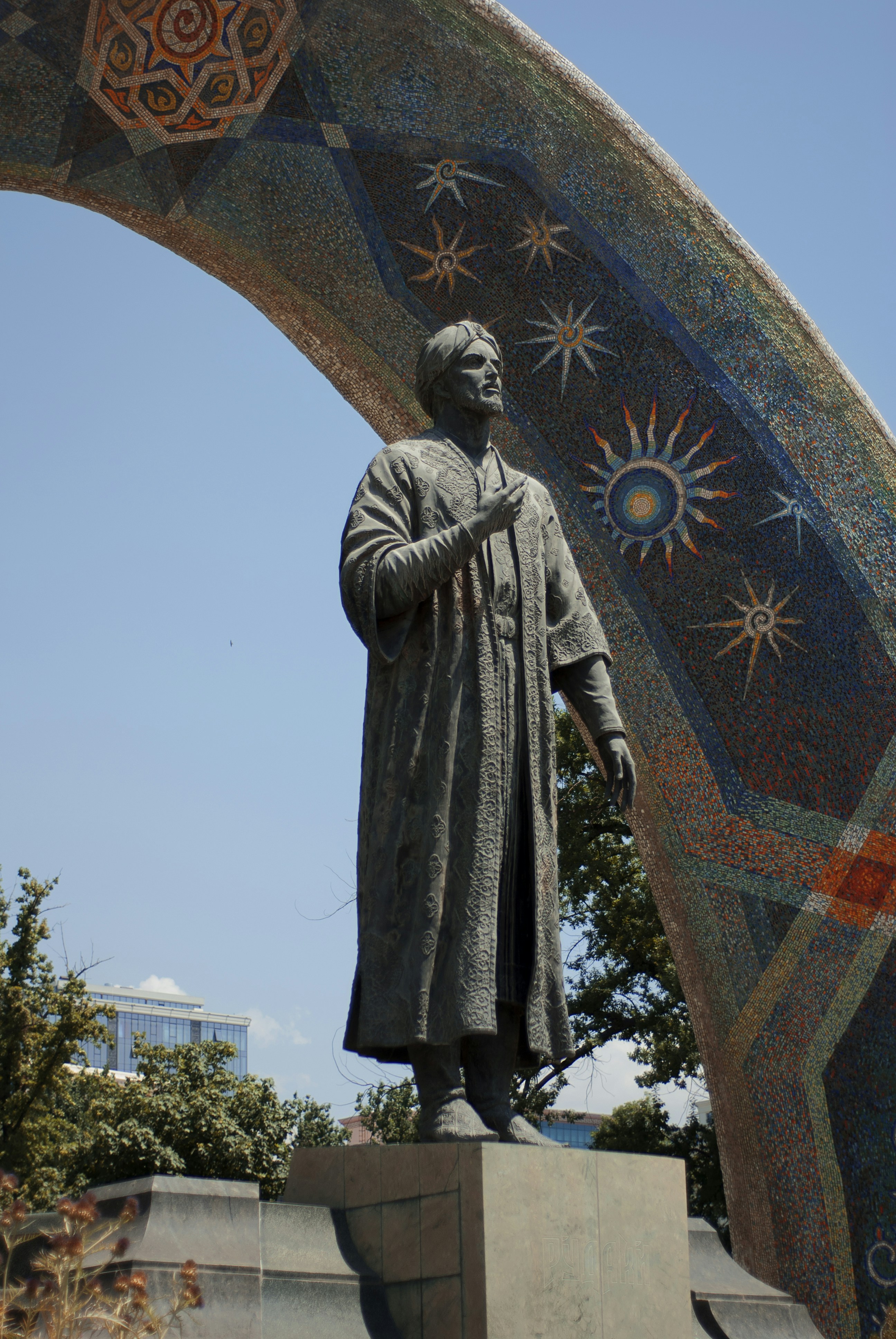 Bronze statue of a historical figure standing proudly beneath a vibrant mosaic arch, symbolizing cultural heritage.
