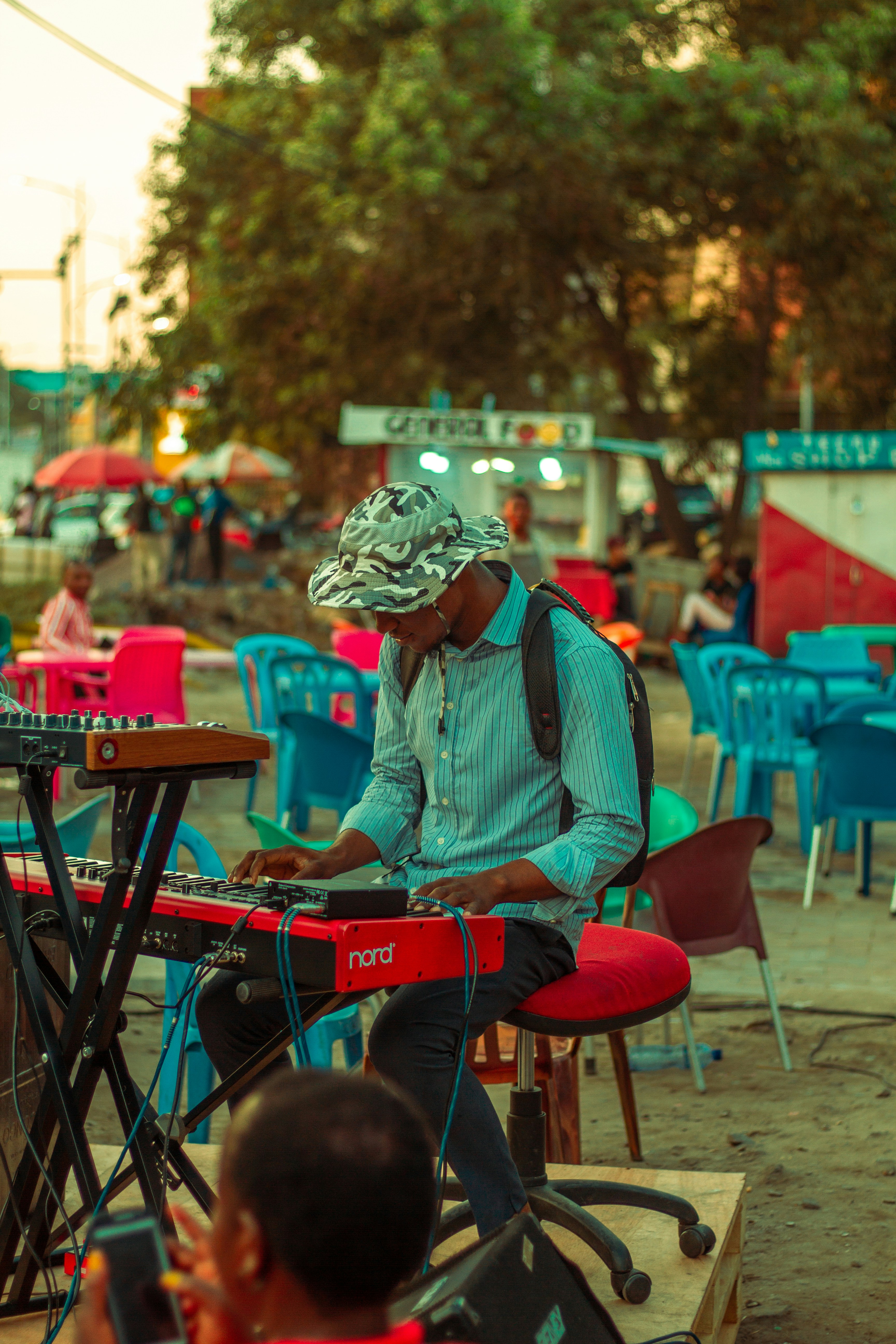 Nord Keys at a Sunlit Street Café: A Solo Keyboardist Among Bright Plastic Chairs