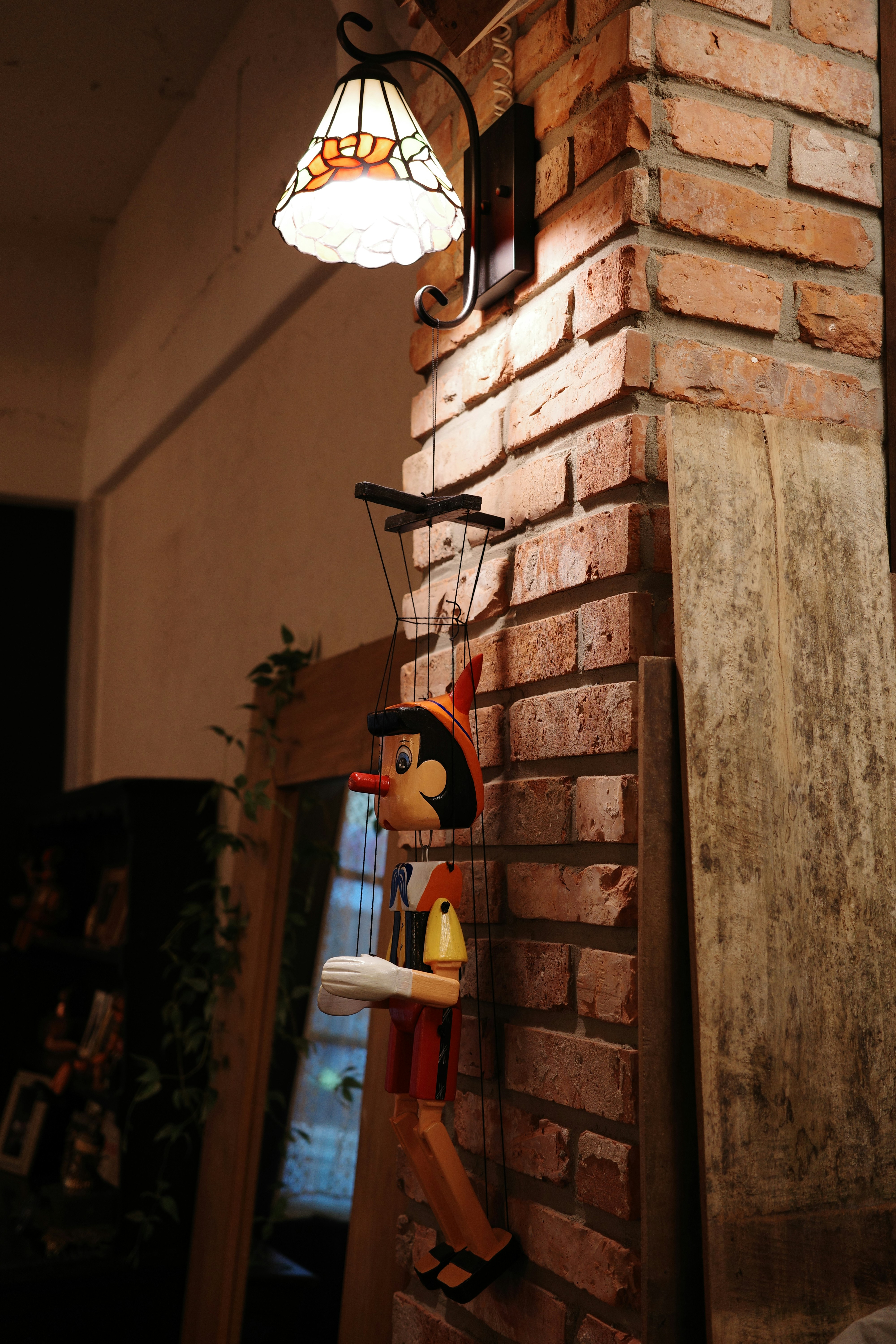 Pinocchio in the Brick Corner: A Warm Interior Moment Beneath a Vintage Lamp