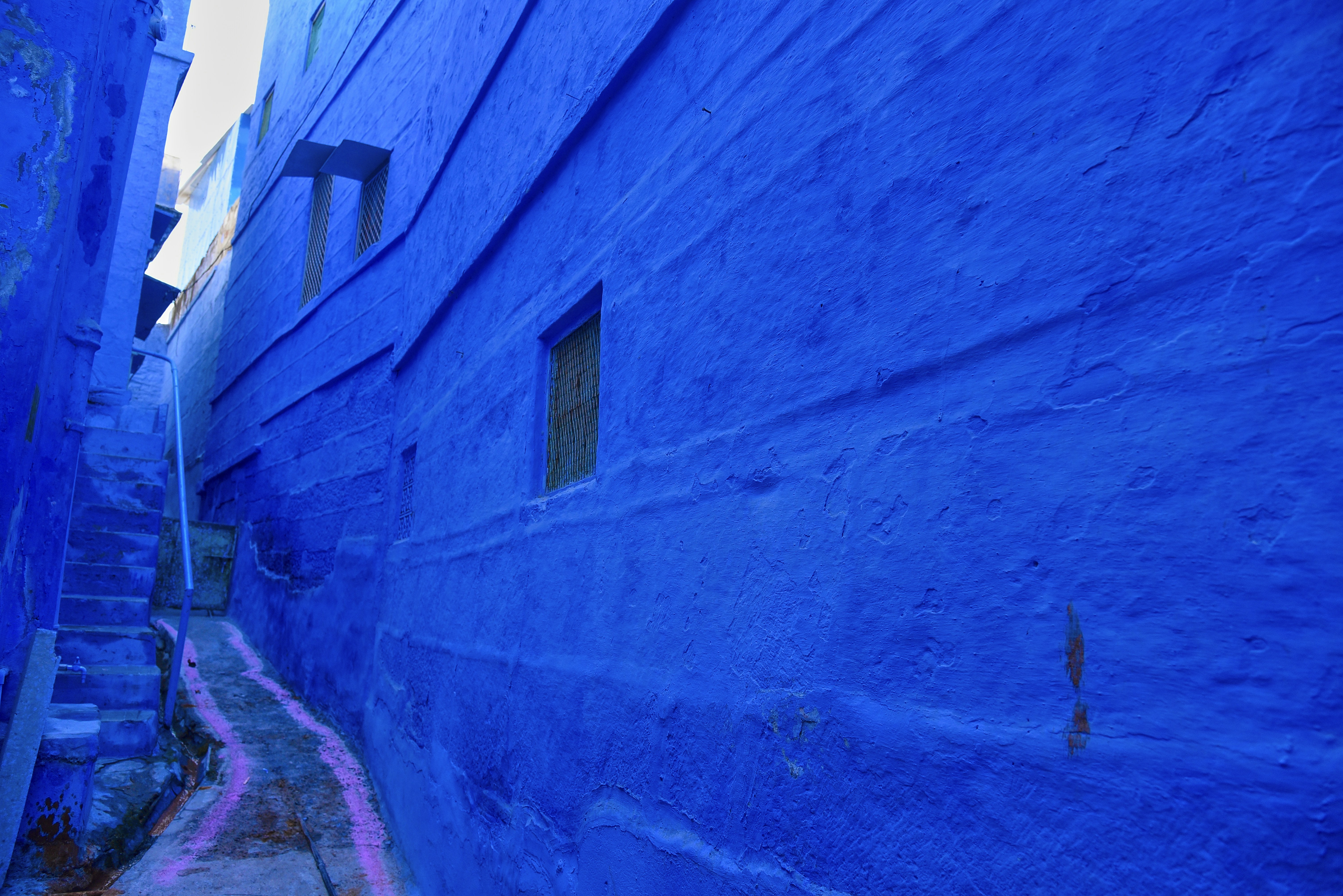 Narrow alley with vibrant blue walls and a staircase leading upward.