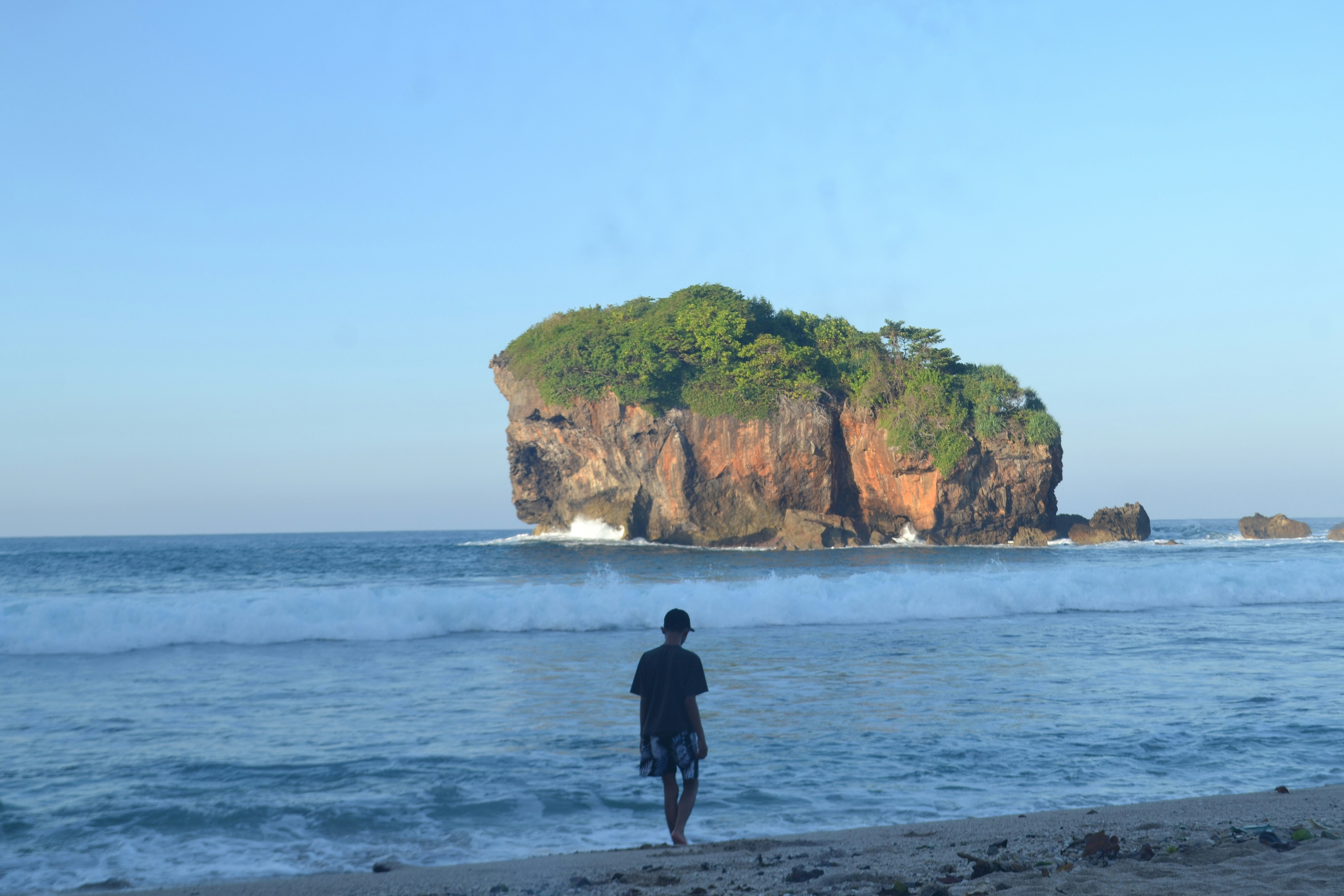 Isolated Island Sentinel: a lone beachgoer faces a rugged rock outcrop