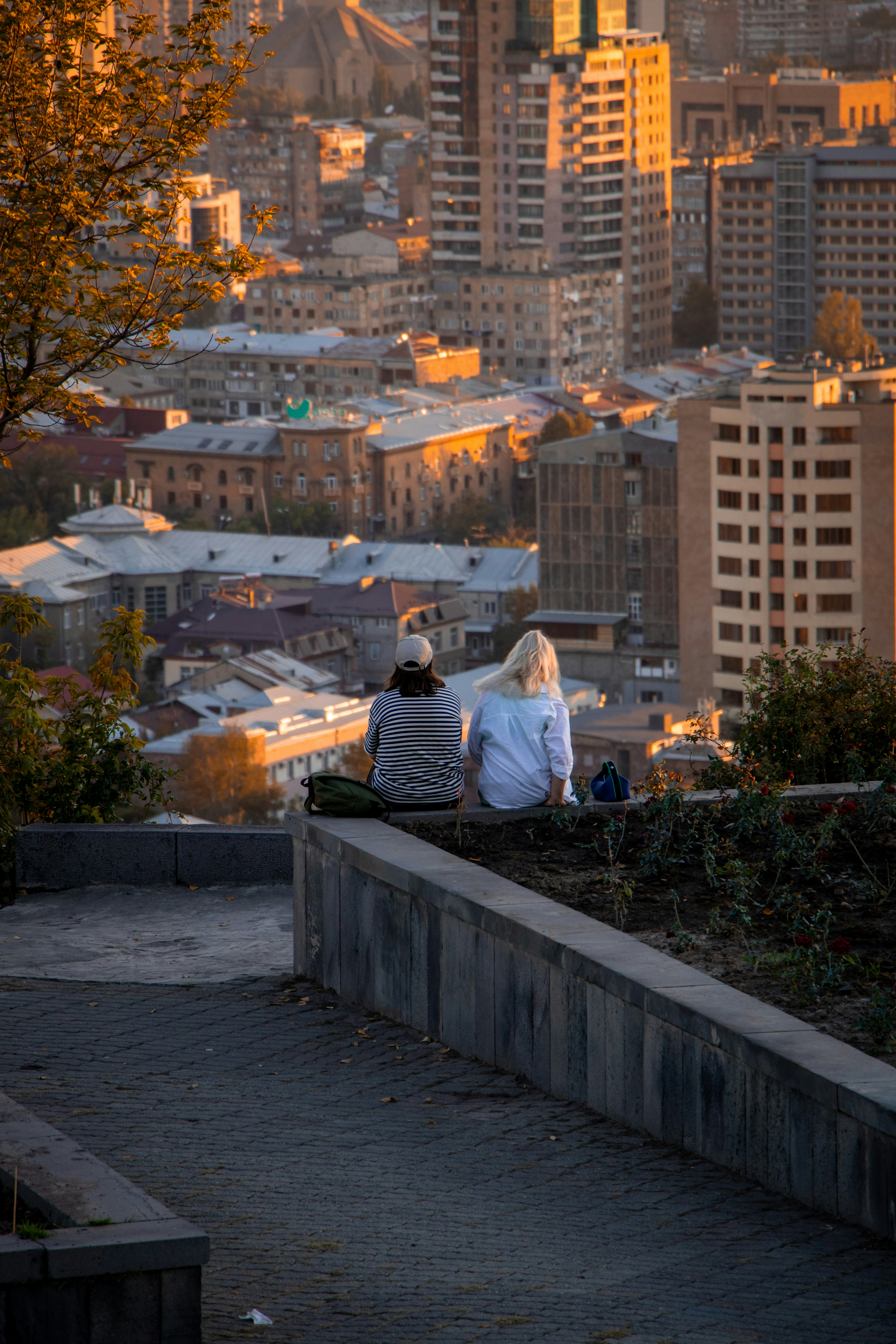 Two people sitting on a ledge overlooking a city photo – Free City ...