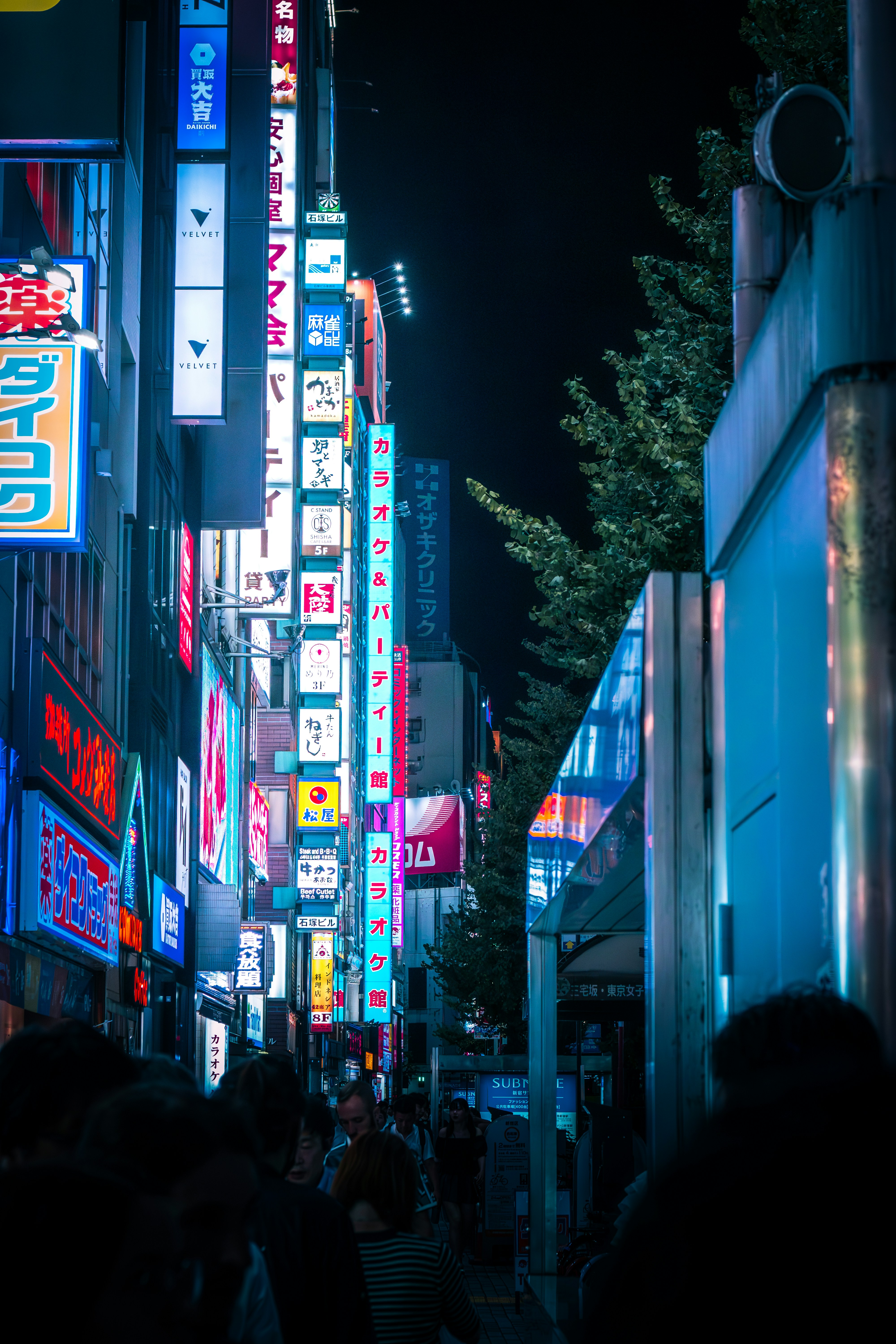 Vibrant city street illuminated by neon signs, bustling with pedestrians at night. The scene captures the essence of urban nightlife.