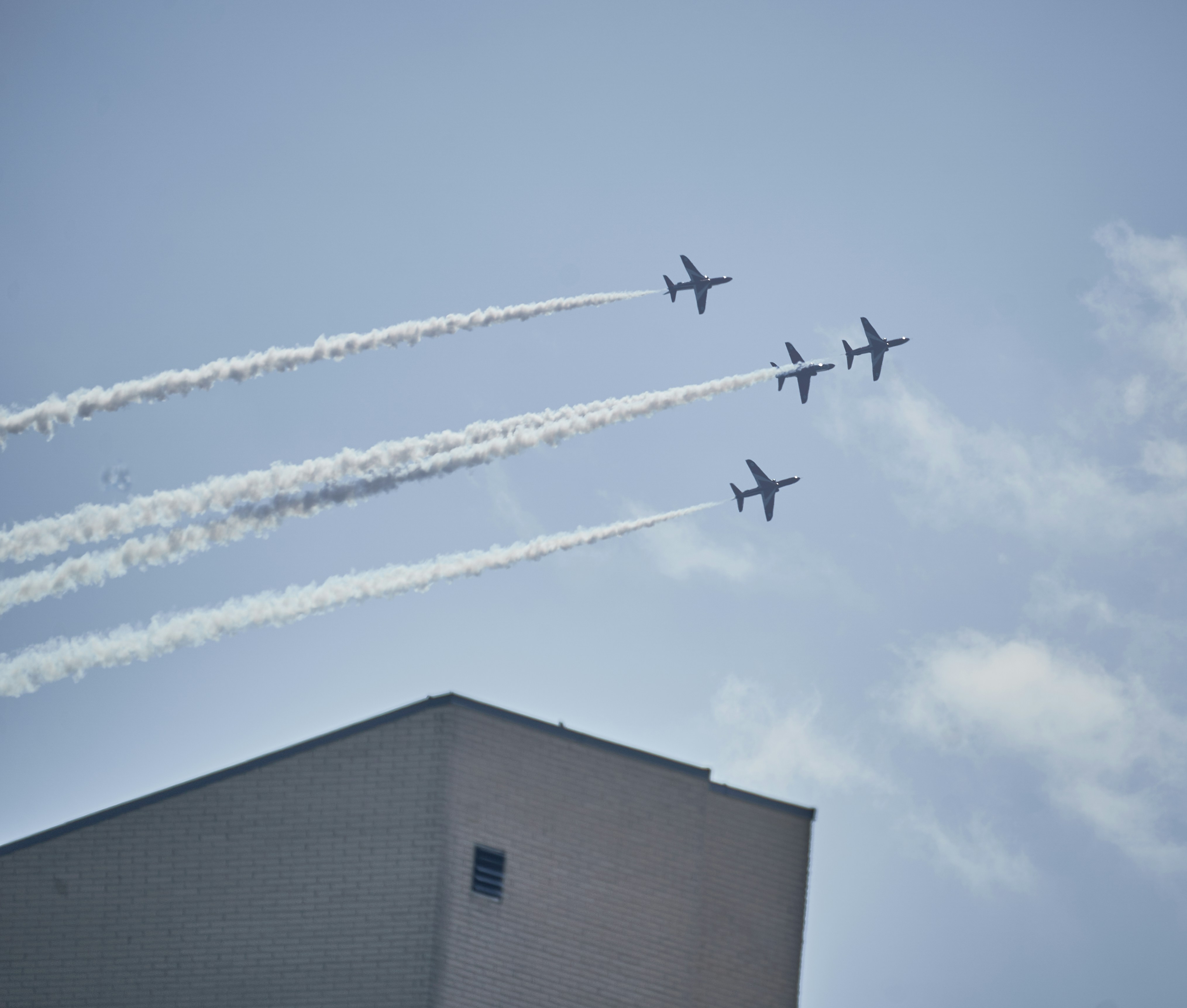 Skybound Quartet: Four jets trace white ribbons over a rooftop edge