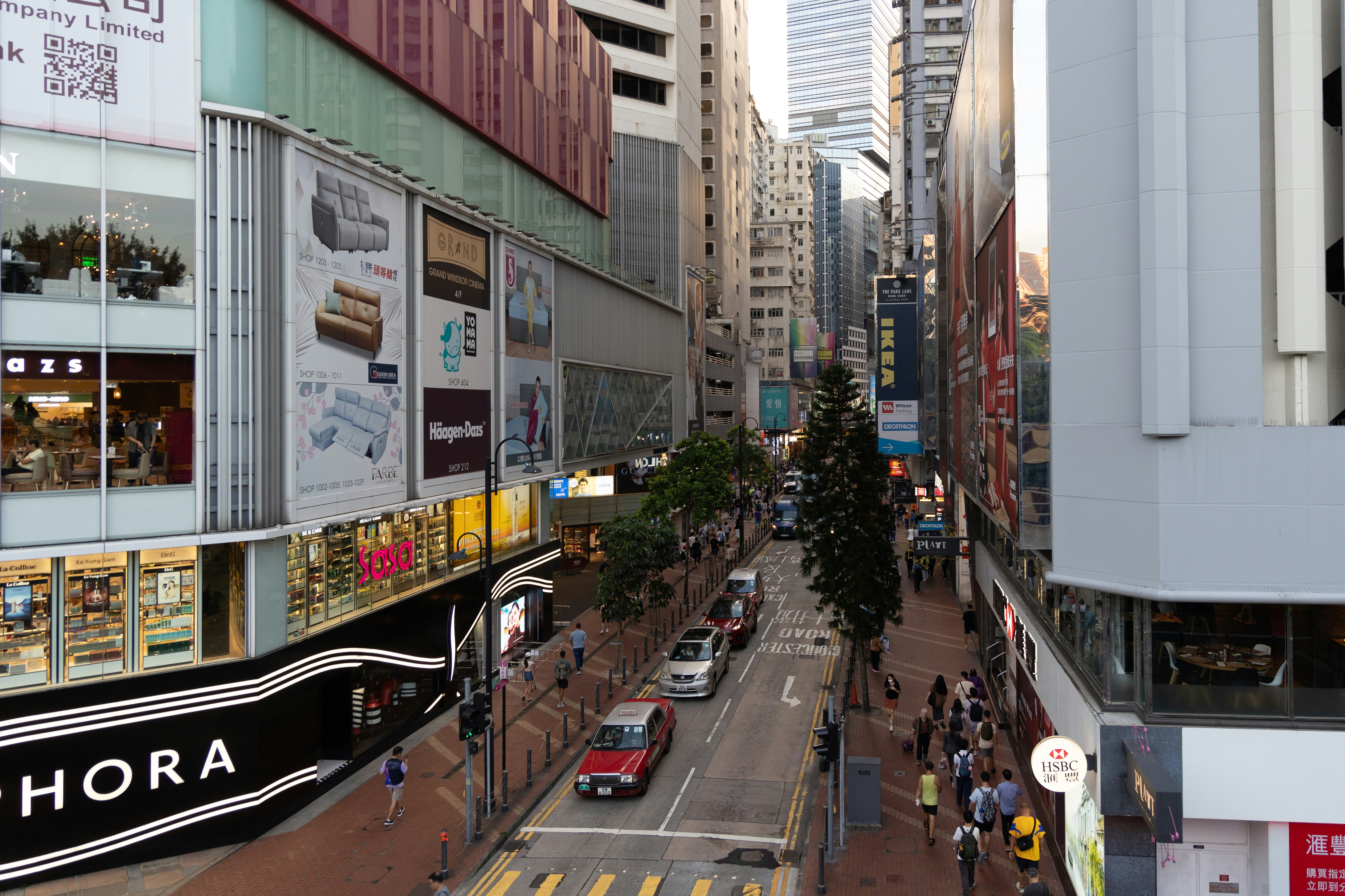 Bustling city street flanked by towering buildings and vibrant billboards under soft evening light.
