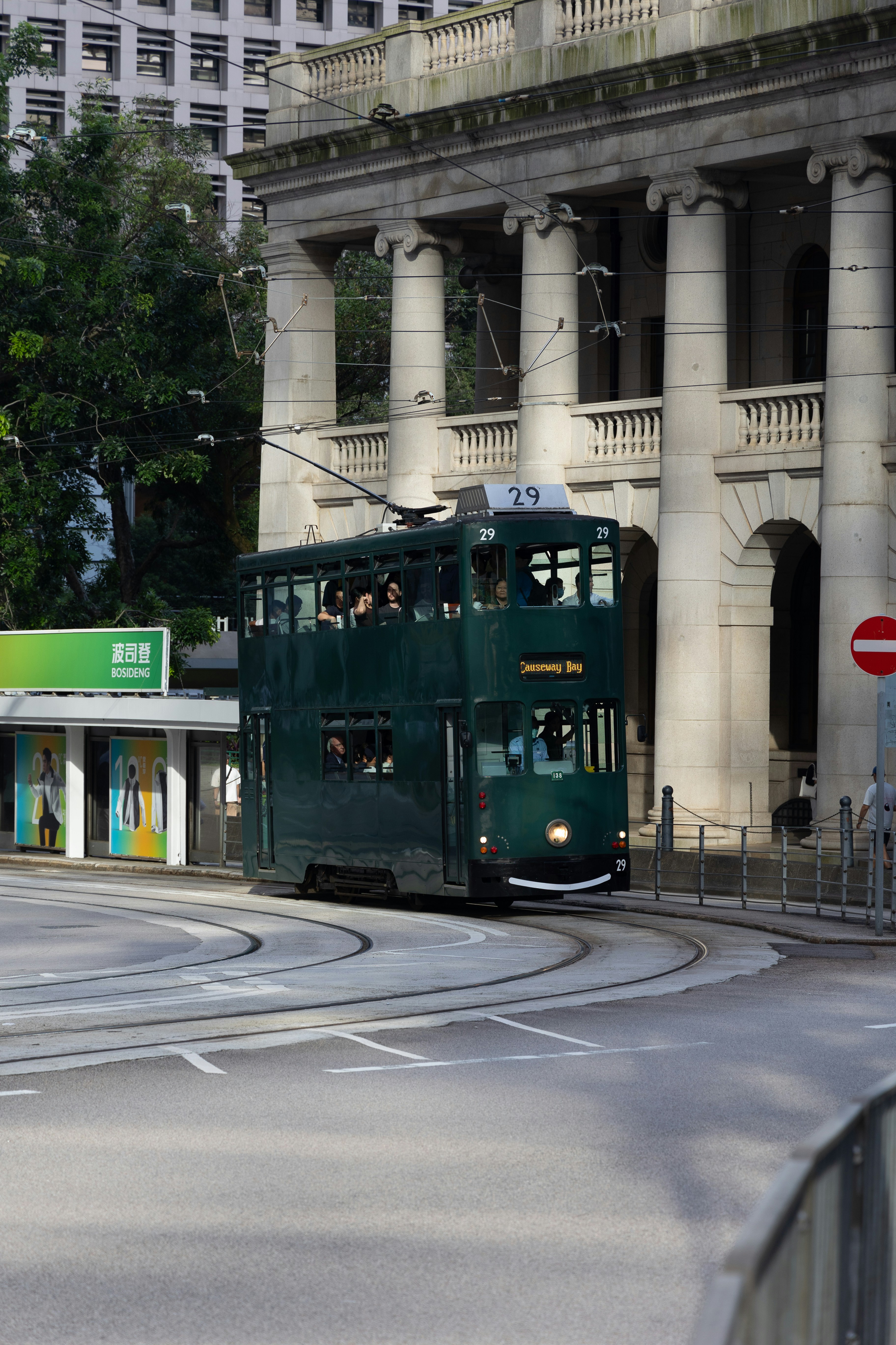 A green trolley driving down a street next to a tall building photo ...