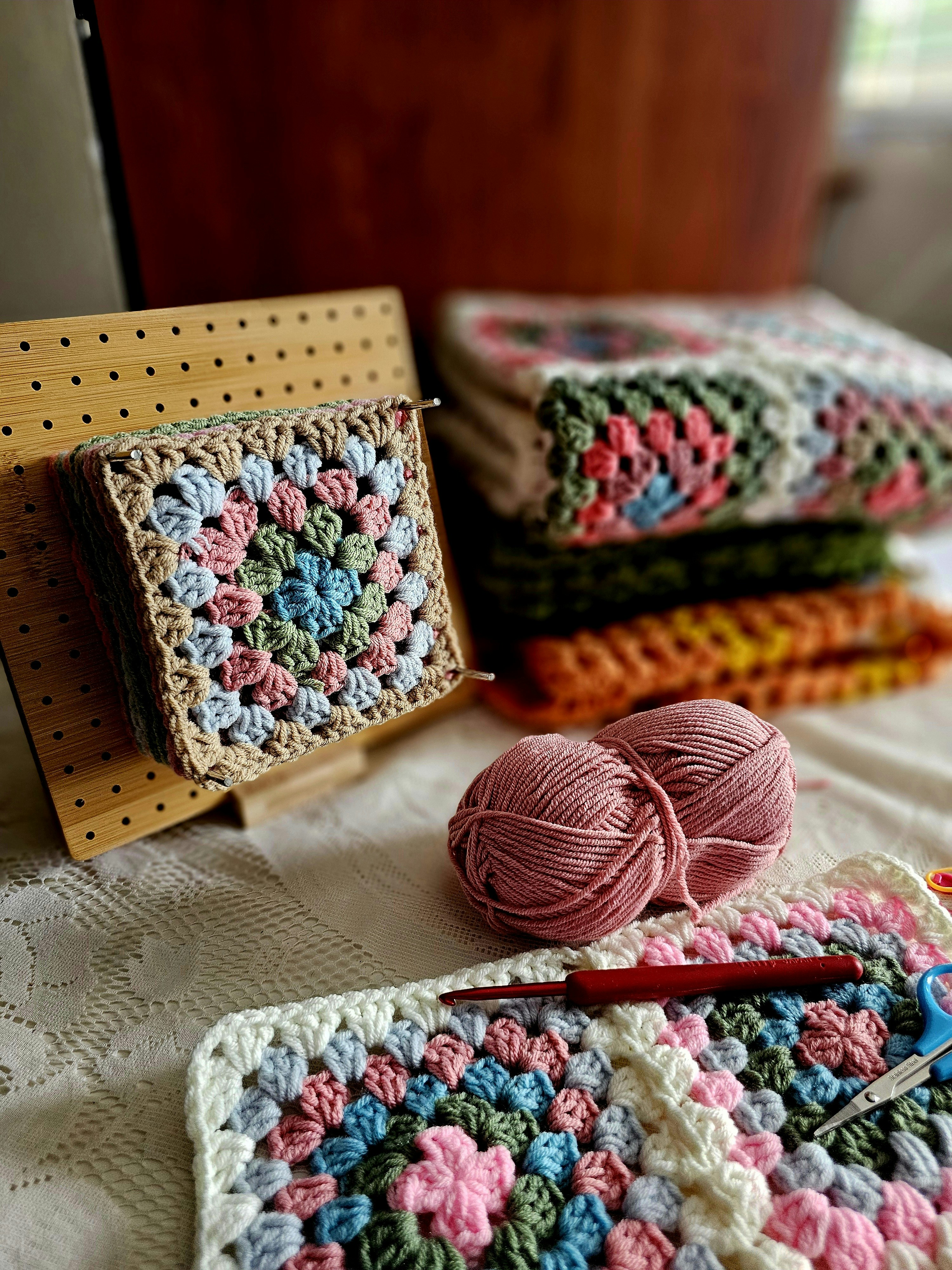 Colorful crochet squares and yarn arranged on a lace tablecloth, showcasing the art of textile crafting.