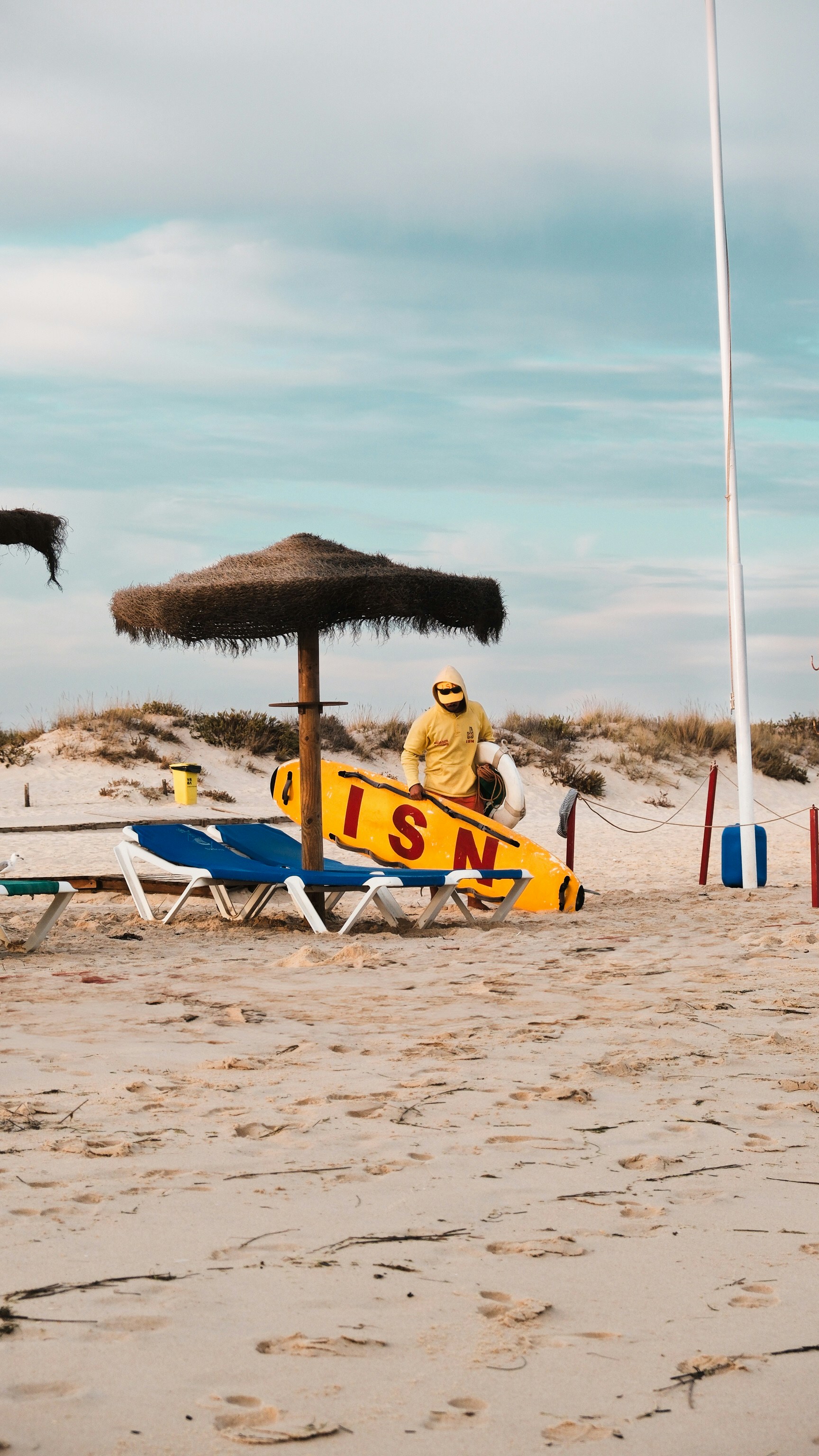 Sunlit Lifeguard Moment: Yellow Vessel and Straw Shelter on Quiet Beach