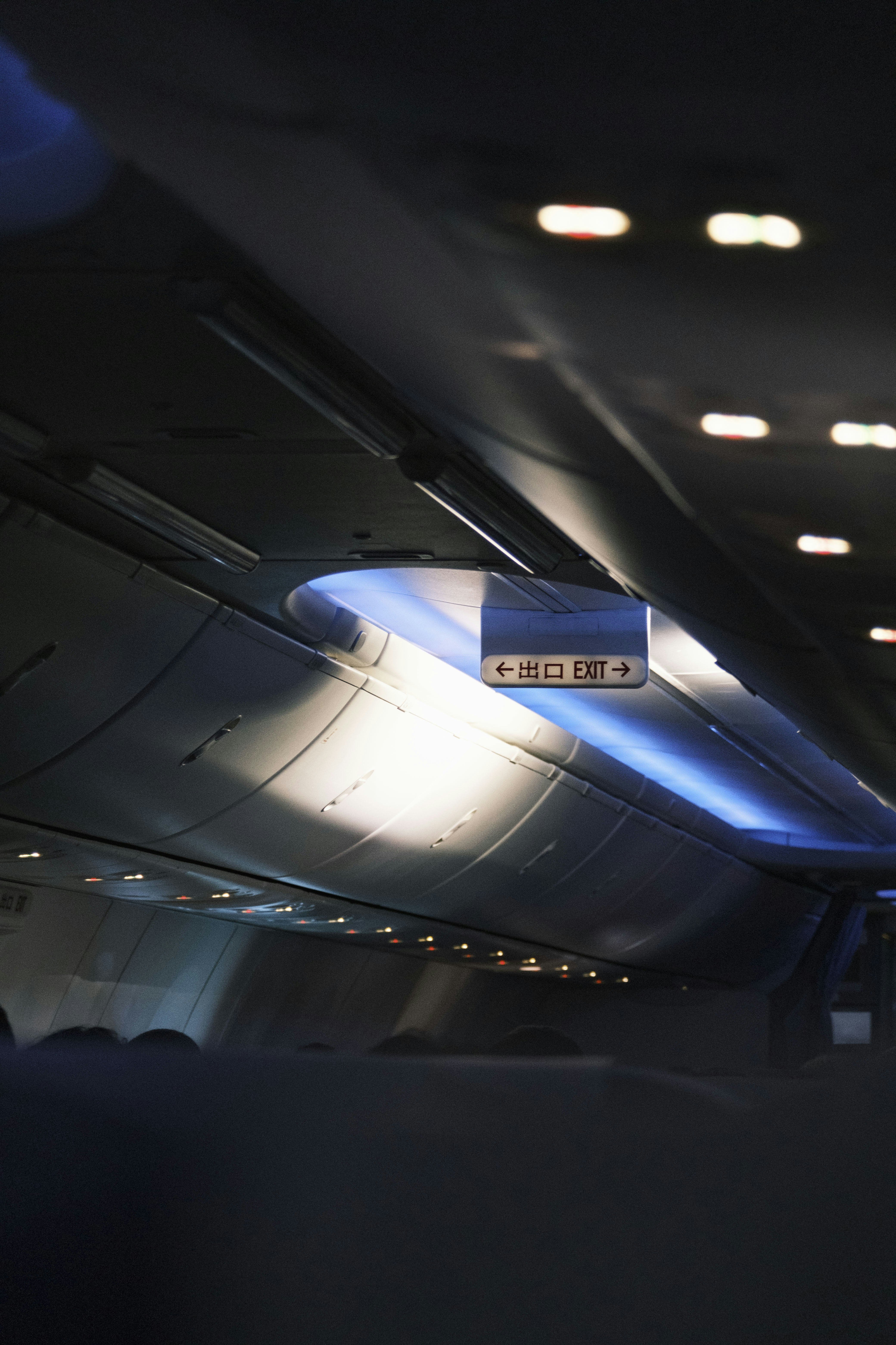 Exit Sign in the Narrow Aisle: Blue Neon Reflections on Curved Cabin Walls