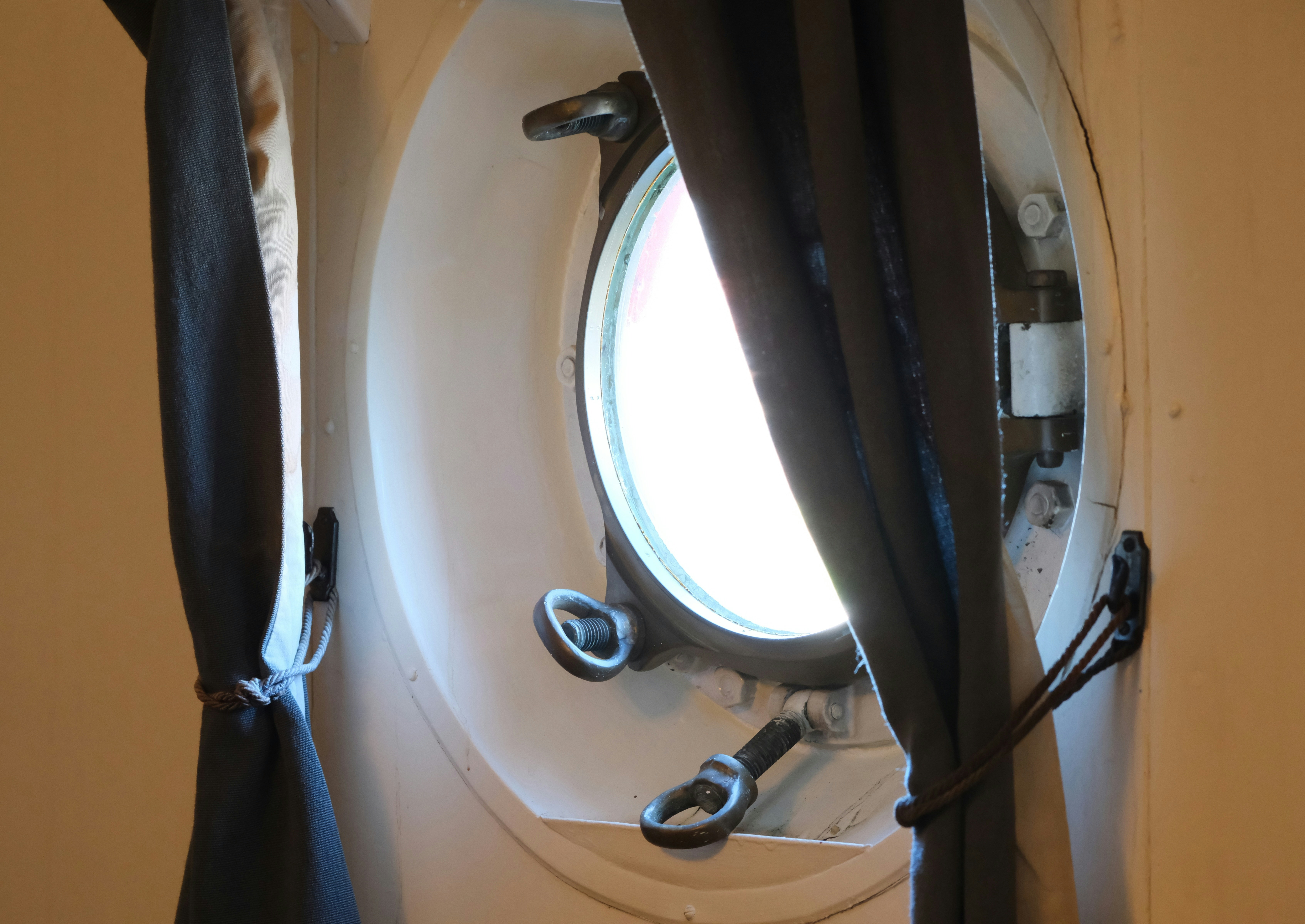 Cobalt daylight at a circular cabin porthole framed by curtains