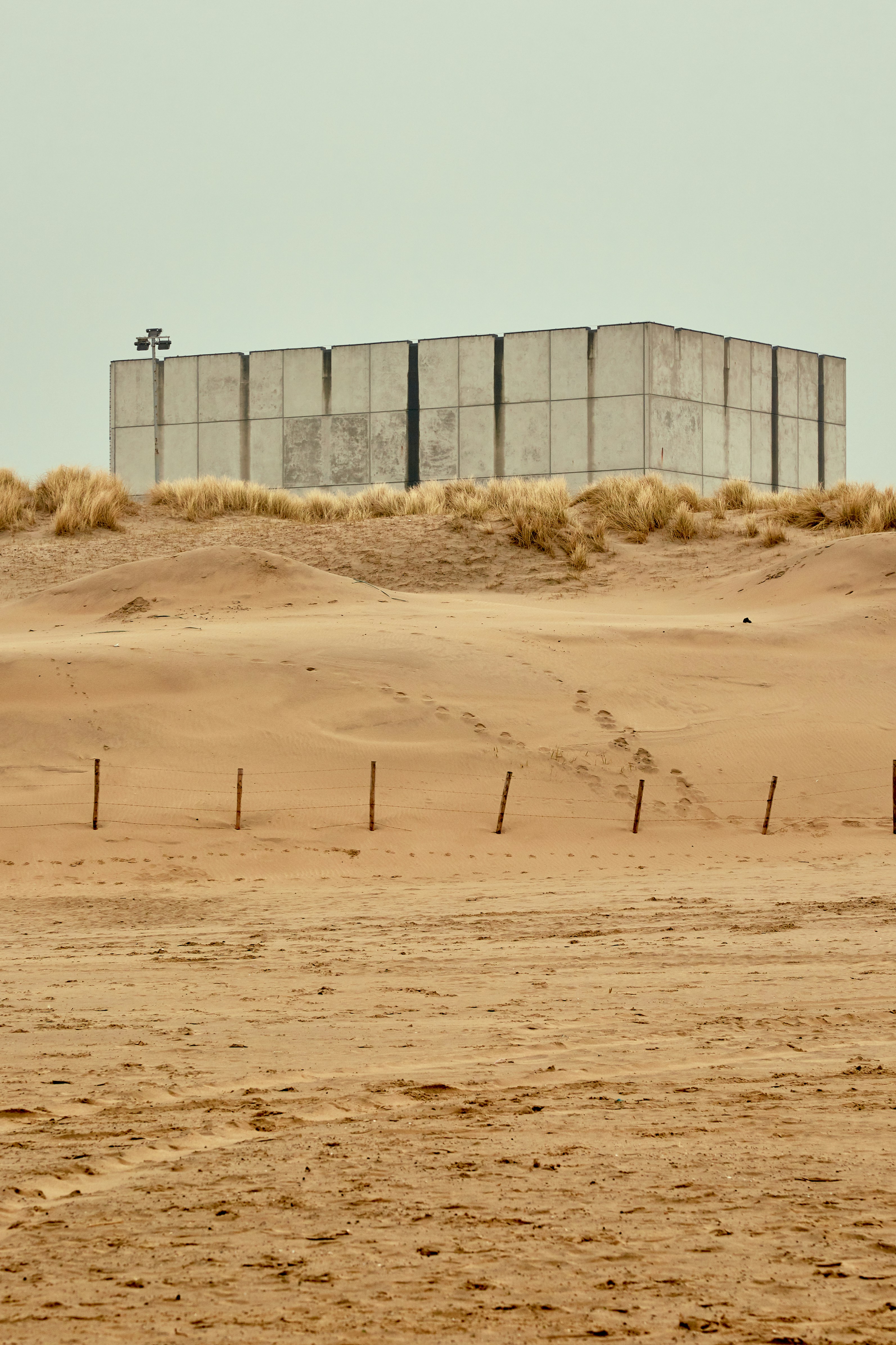 The Dune Sentinel: Concrete Barrier Framing a Desert Silence