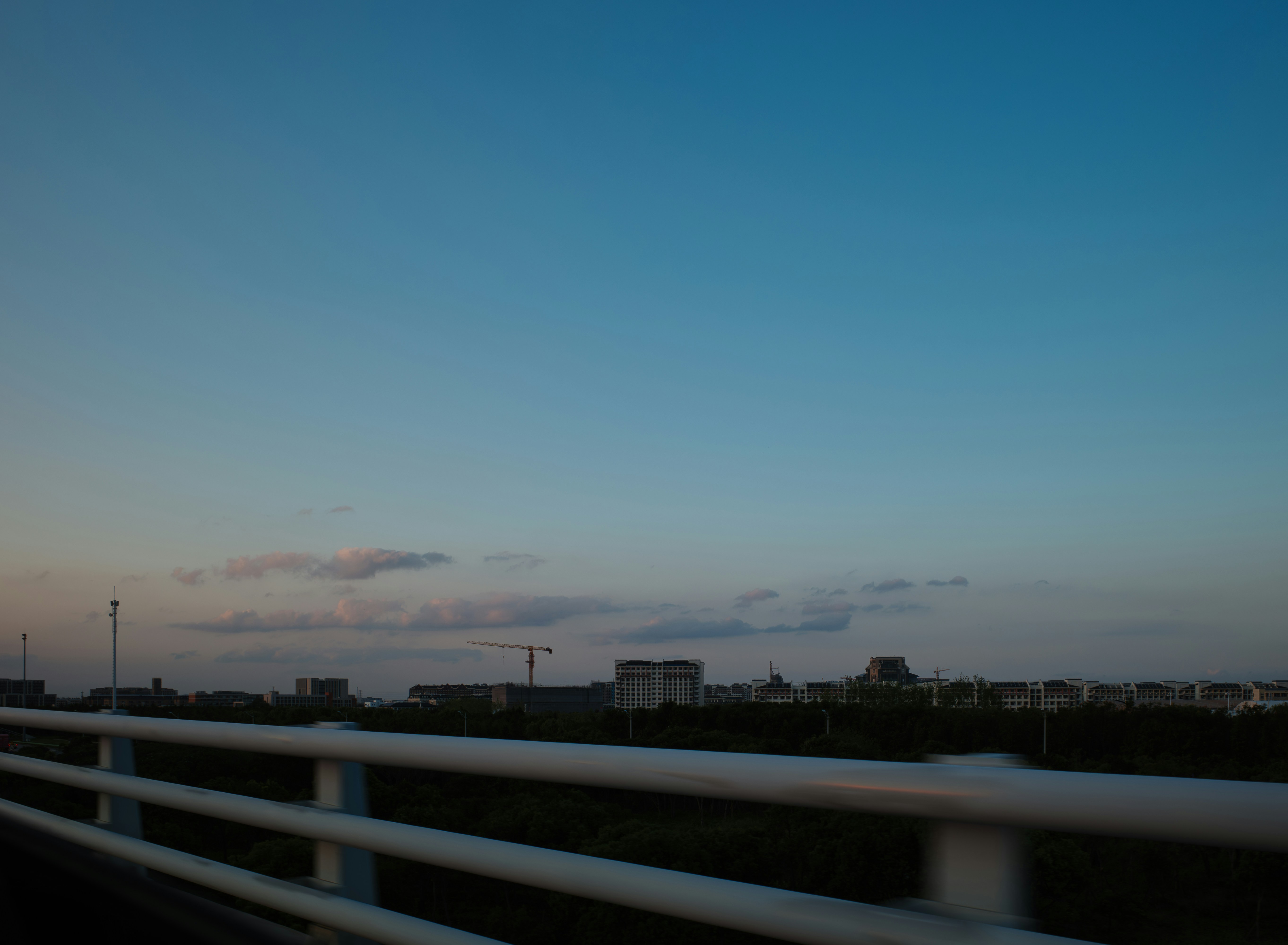 A panoramic view of a city skyline under a twilight sky, with silhouetted buildings and a distant crane. The scene captures the transition from day to night.