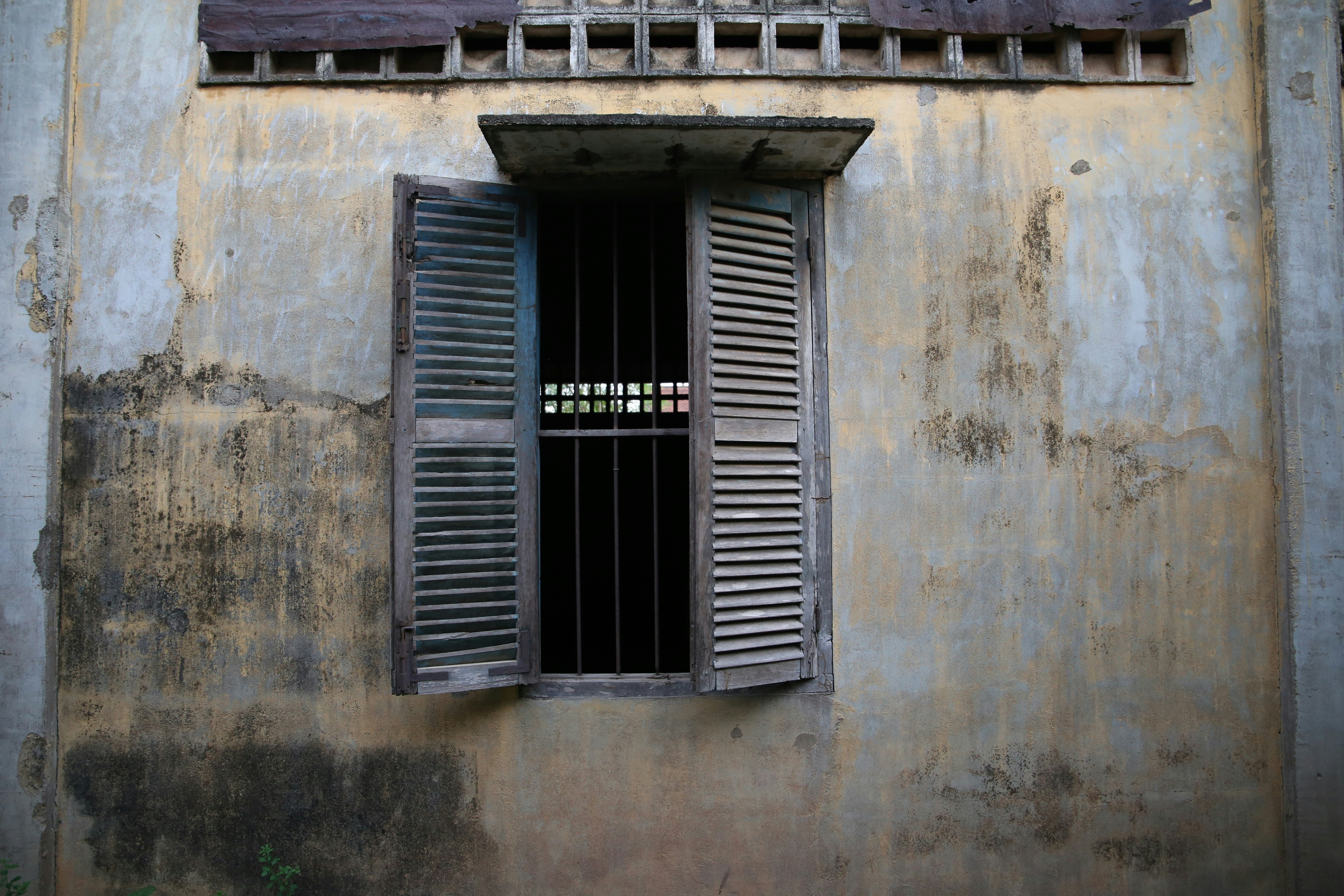 Whispers Through the Shutters: A Weathered Window in a Faded Facade