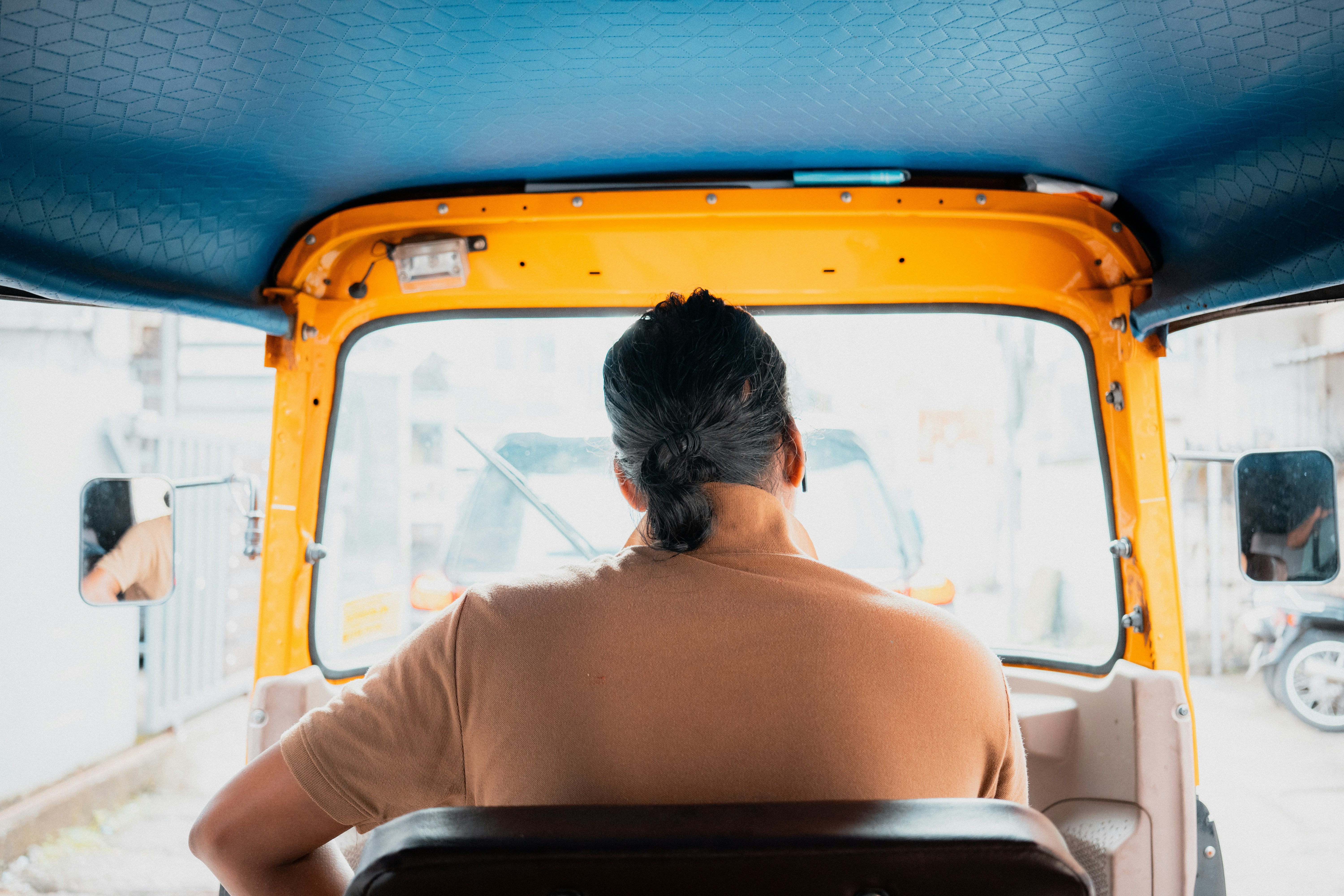 View from the backseat of a rickshaw, capturing the driver’s perspective as they navigate through the streets. The vibrant yellow interior contrasts with the blurred cityscape ahead.