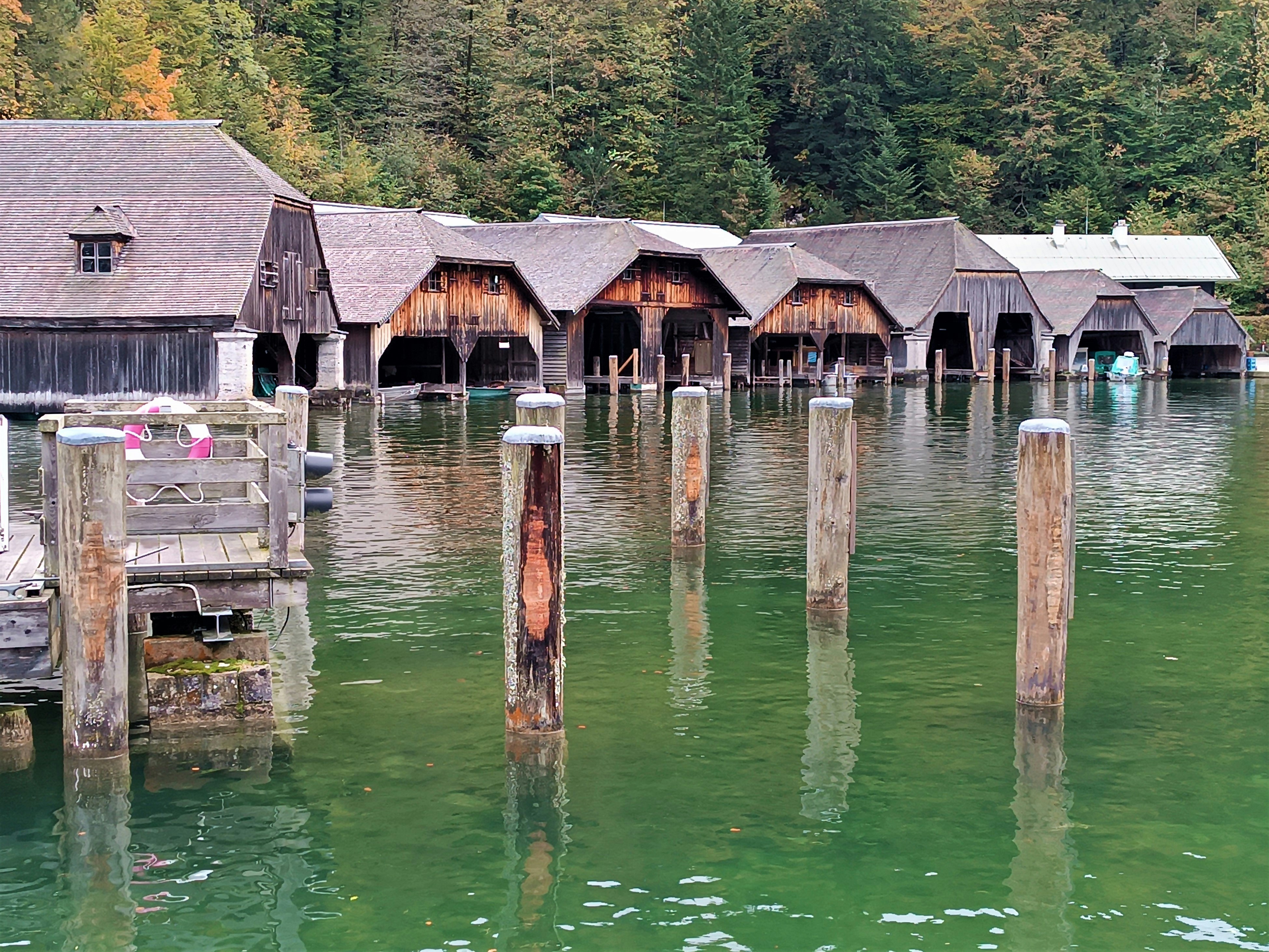 Historic boathouses line a serene lake, their reflections shimmering in emerald waters, framed by lush autumn foliage.