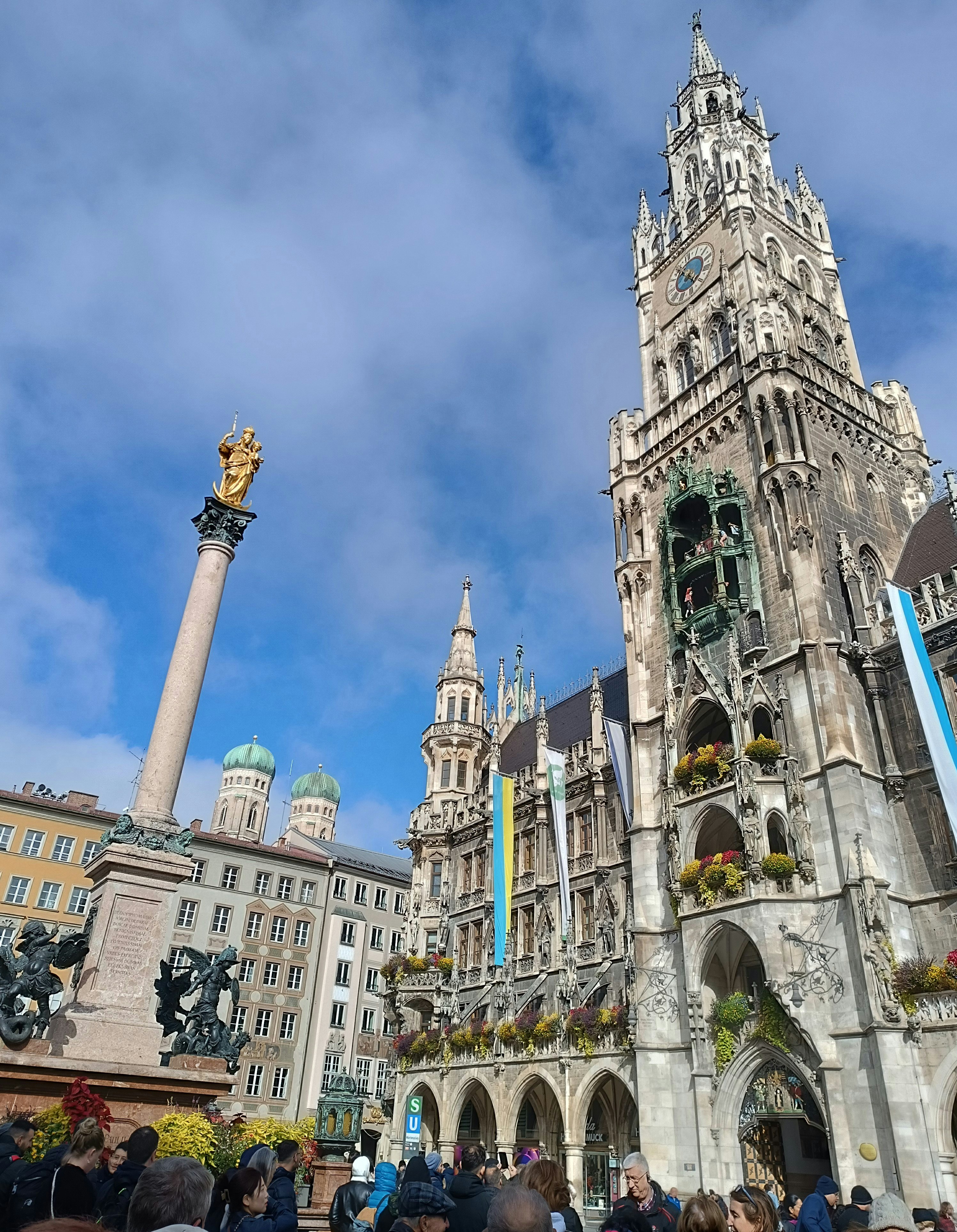 Crowded Marienplatz with the New Town Hall tower on the right and a gilded statue atop a column to the left.
