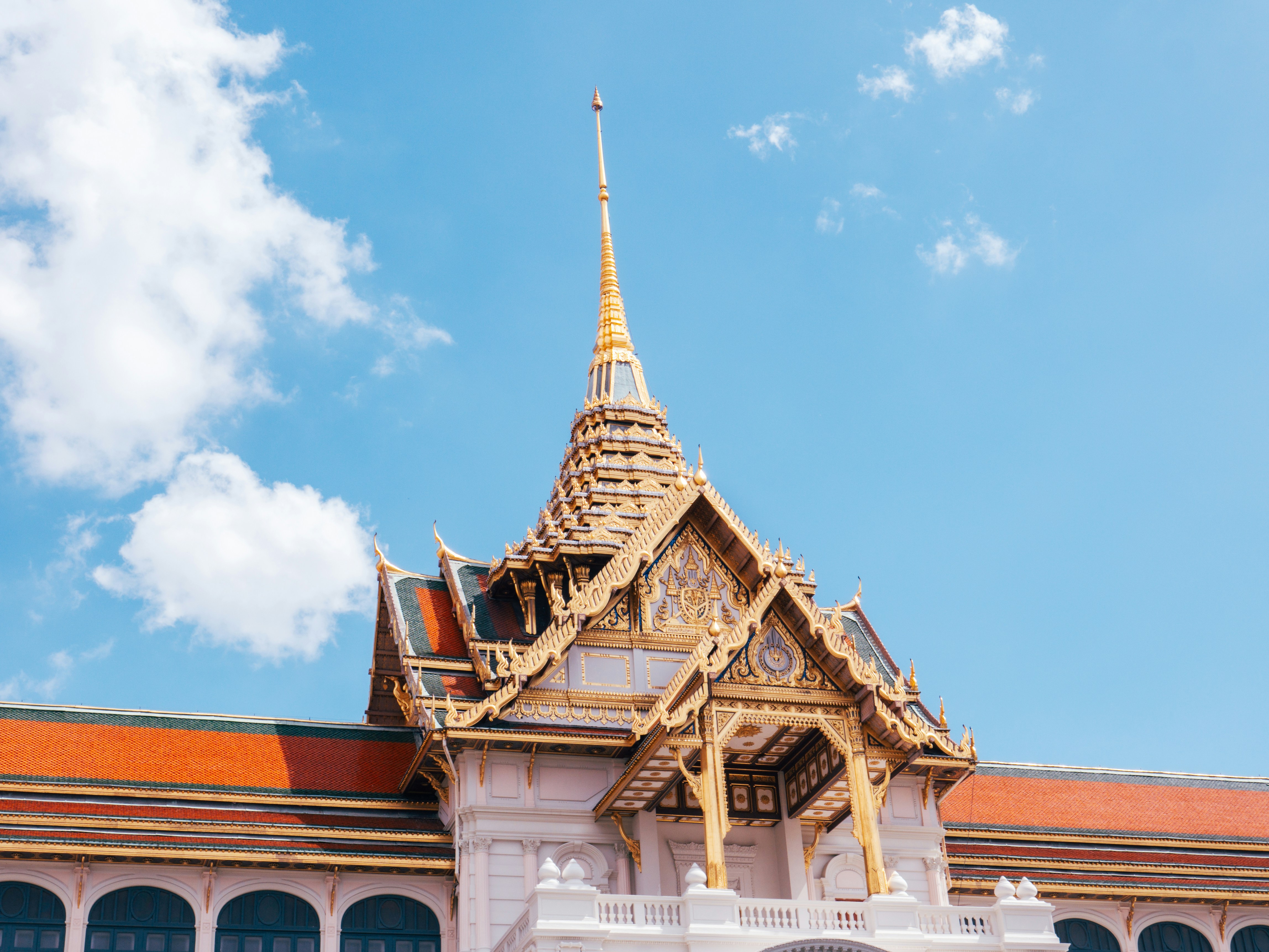 Ornate golden spire tops a traditional building, set against a bright blue sky with scattered clouds.