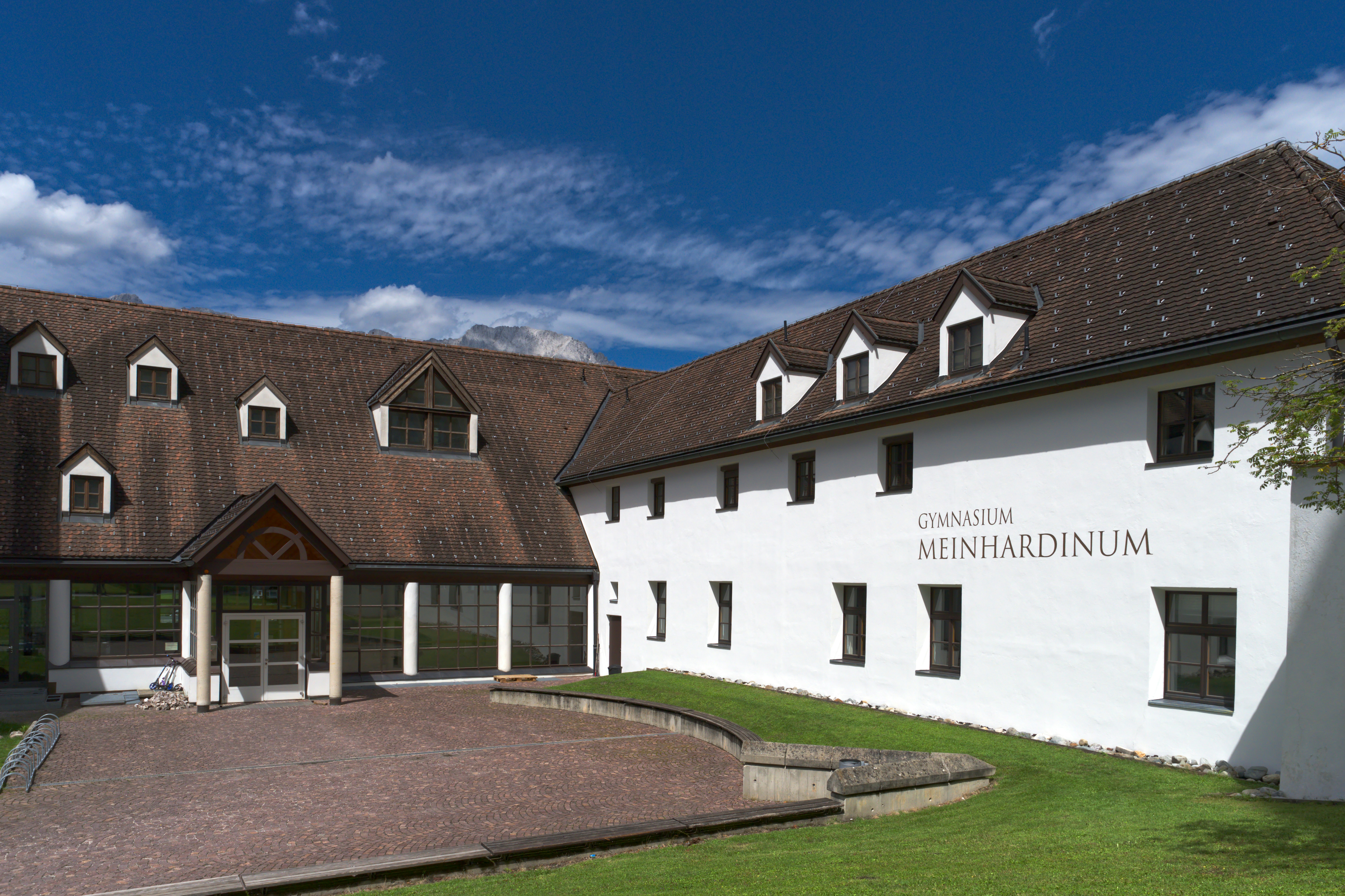 Meinhardinum Gymnasium: Sunlit Campus Facade Framed by a Curved Brick Courtyard