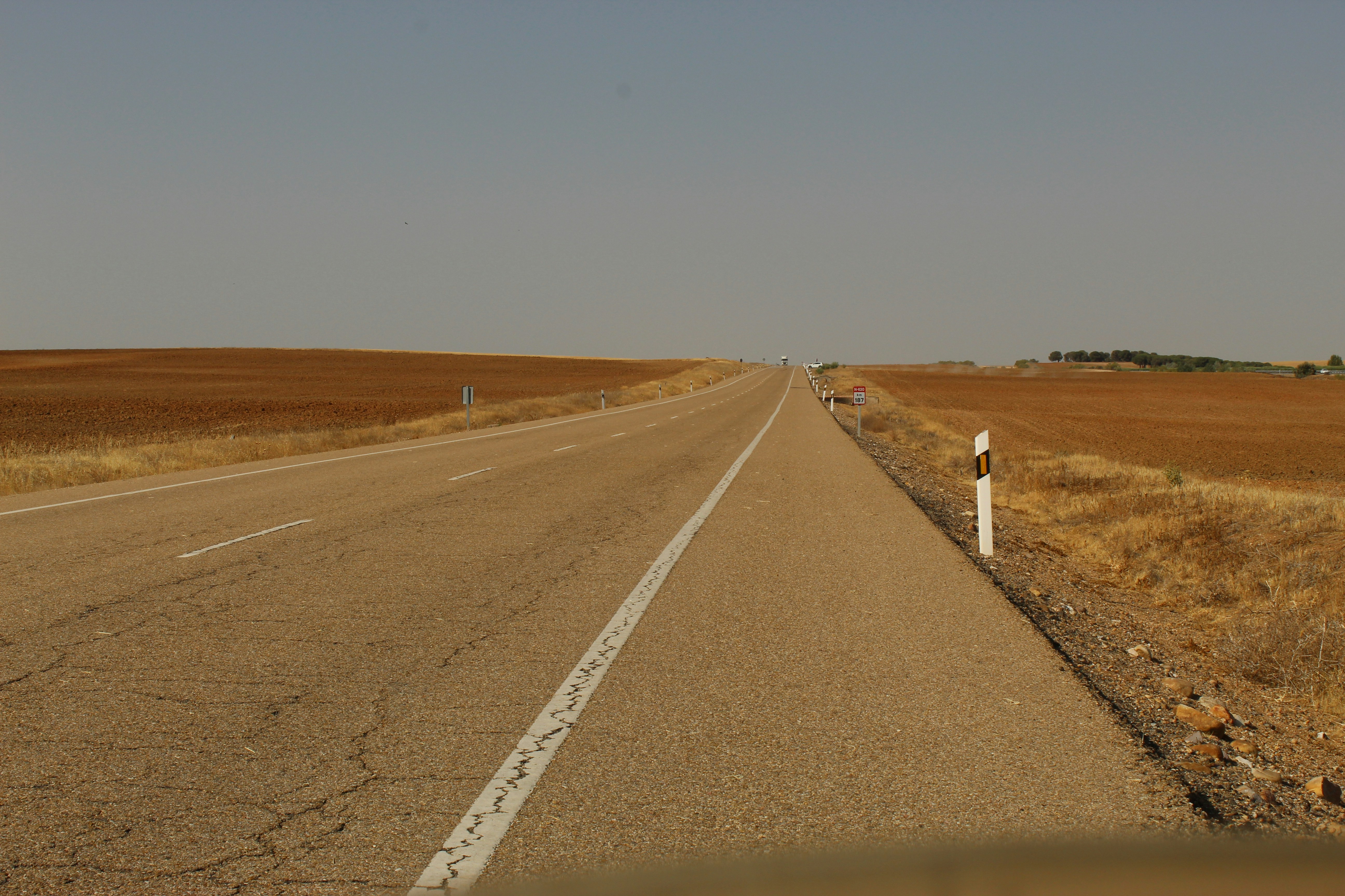 A long, straight highway stretches into the horizon, bordered by vast golden fields under a clear sky.