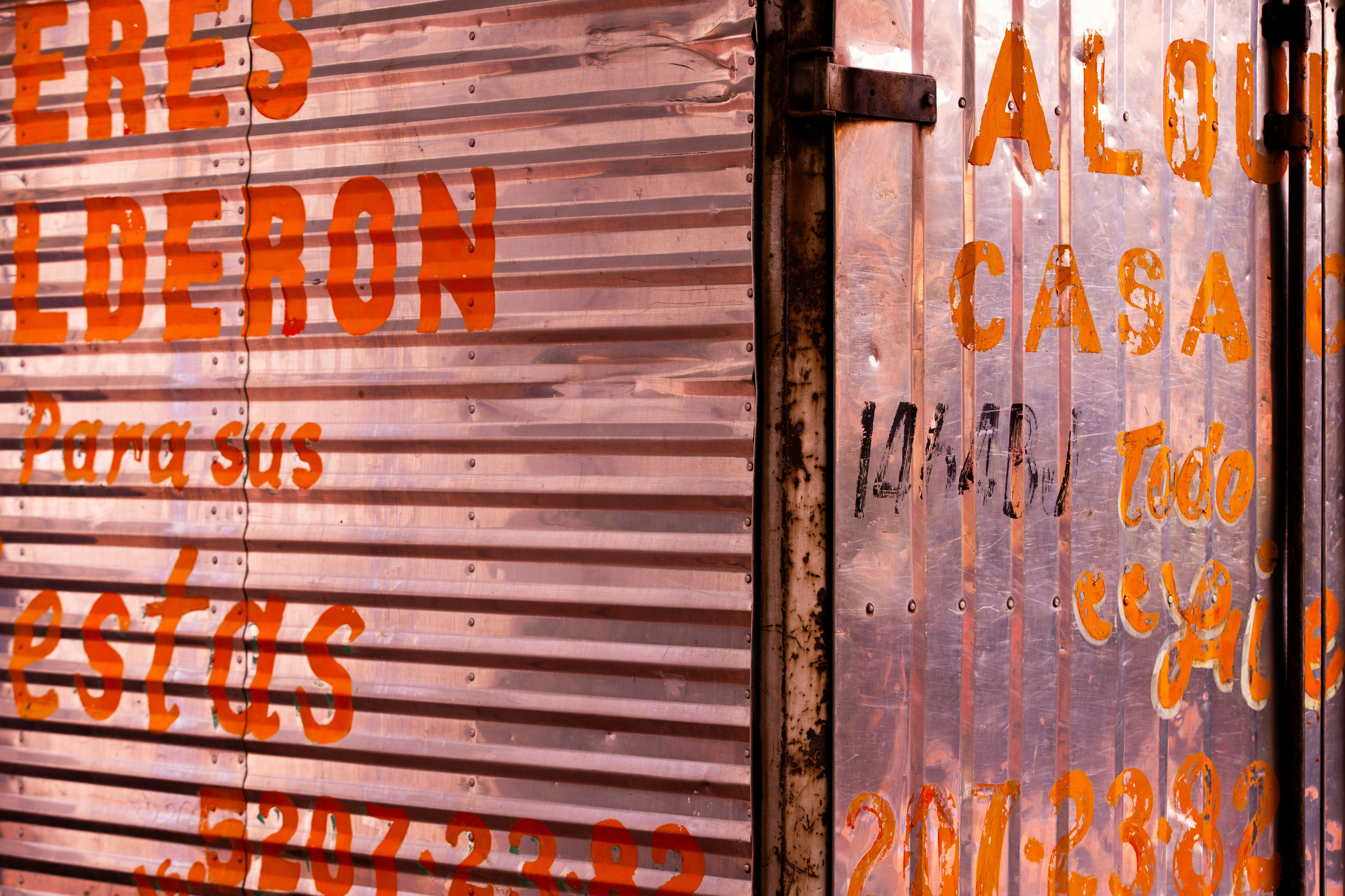 Orange Script on Rusted Corrugations: A Weathered Shutter