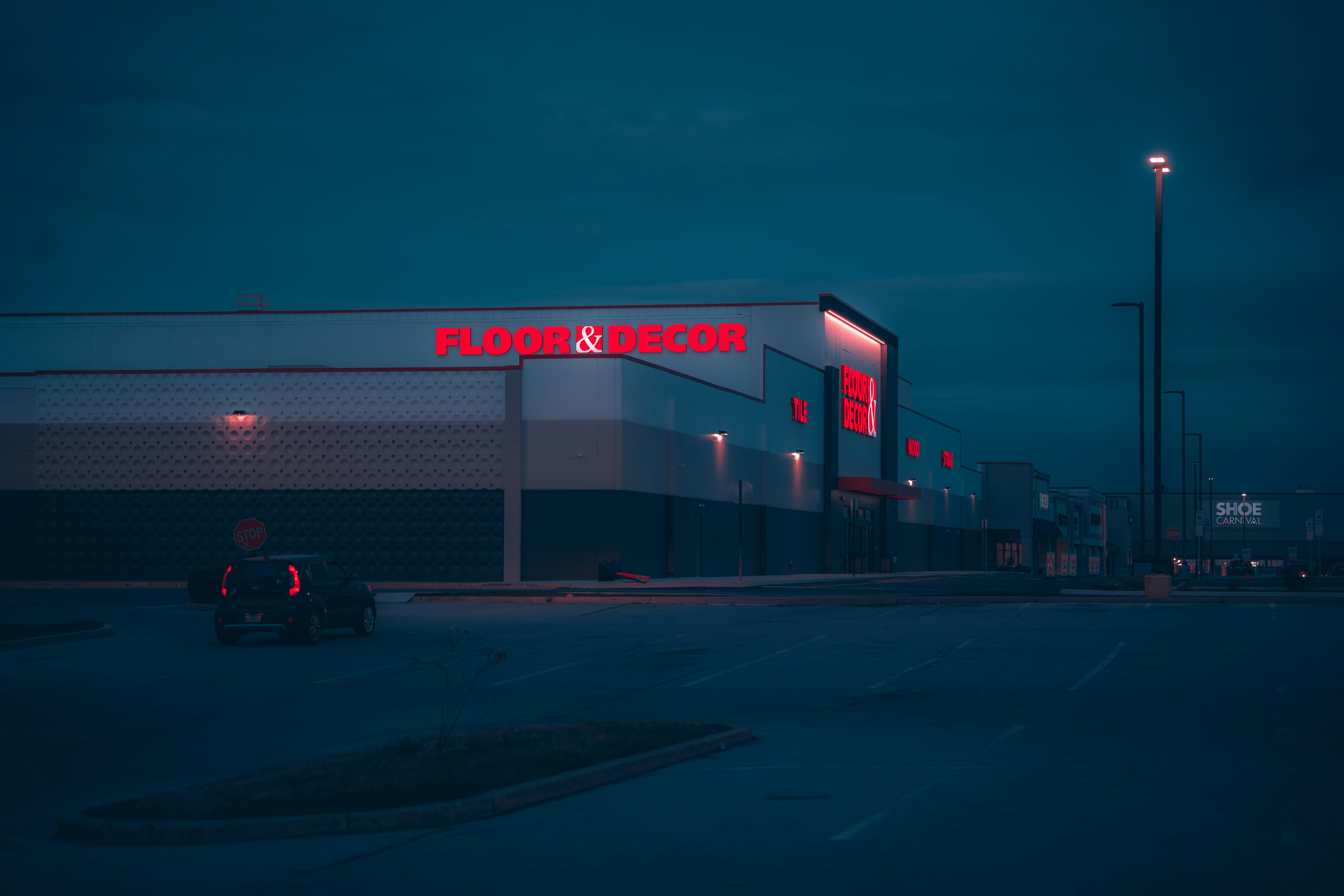 Empty parking lot with a dimly lit building under a dusky sky, highlighted by red neon signage.