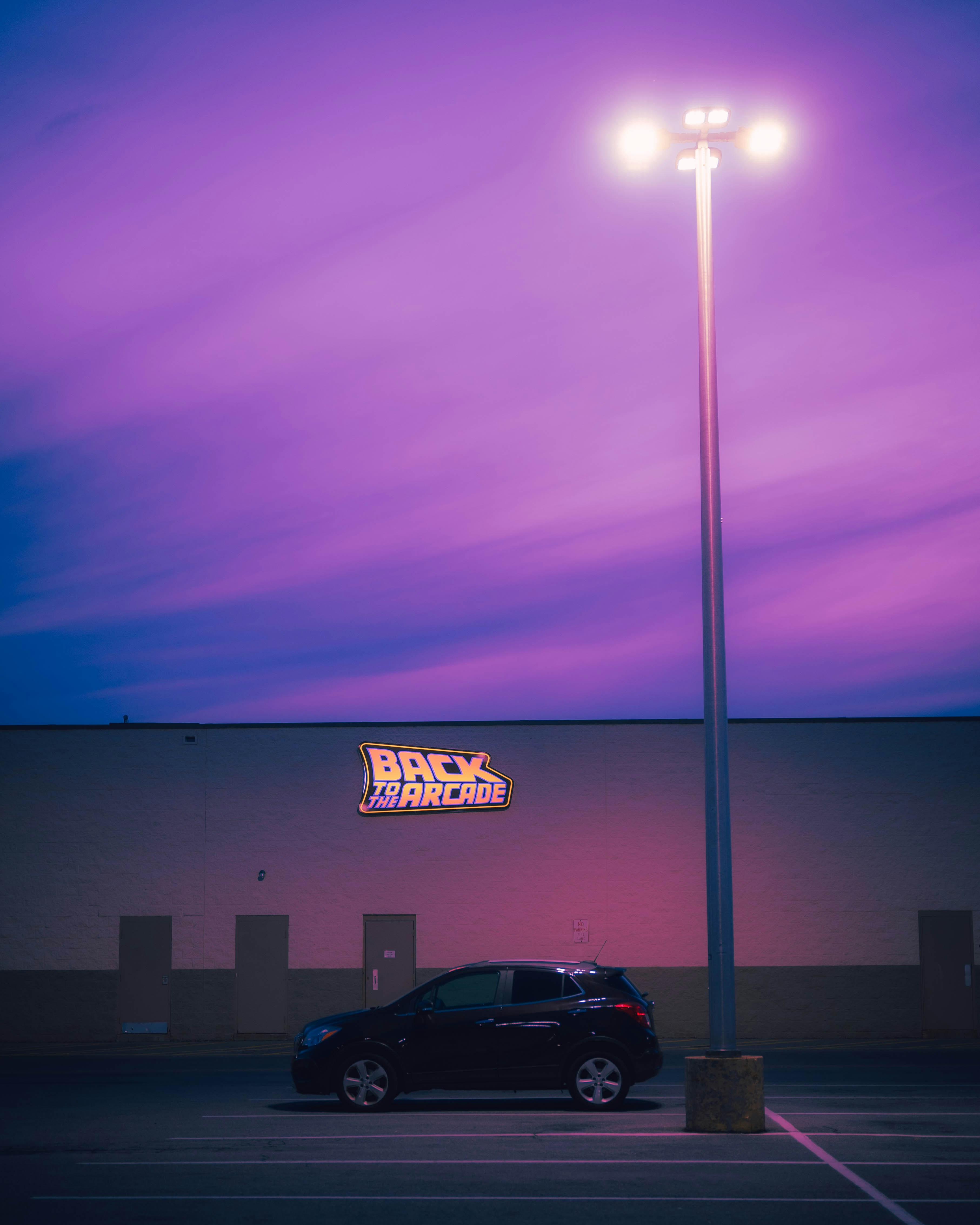 Purple Dusk Over a Quiet Parking Lot with a Lone SUV and Arcade Sign