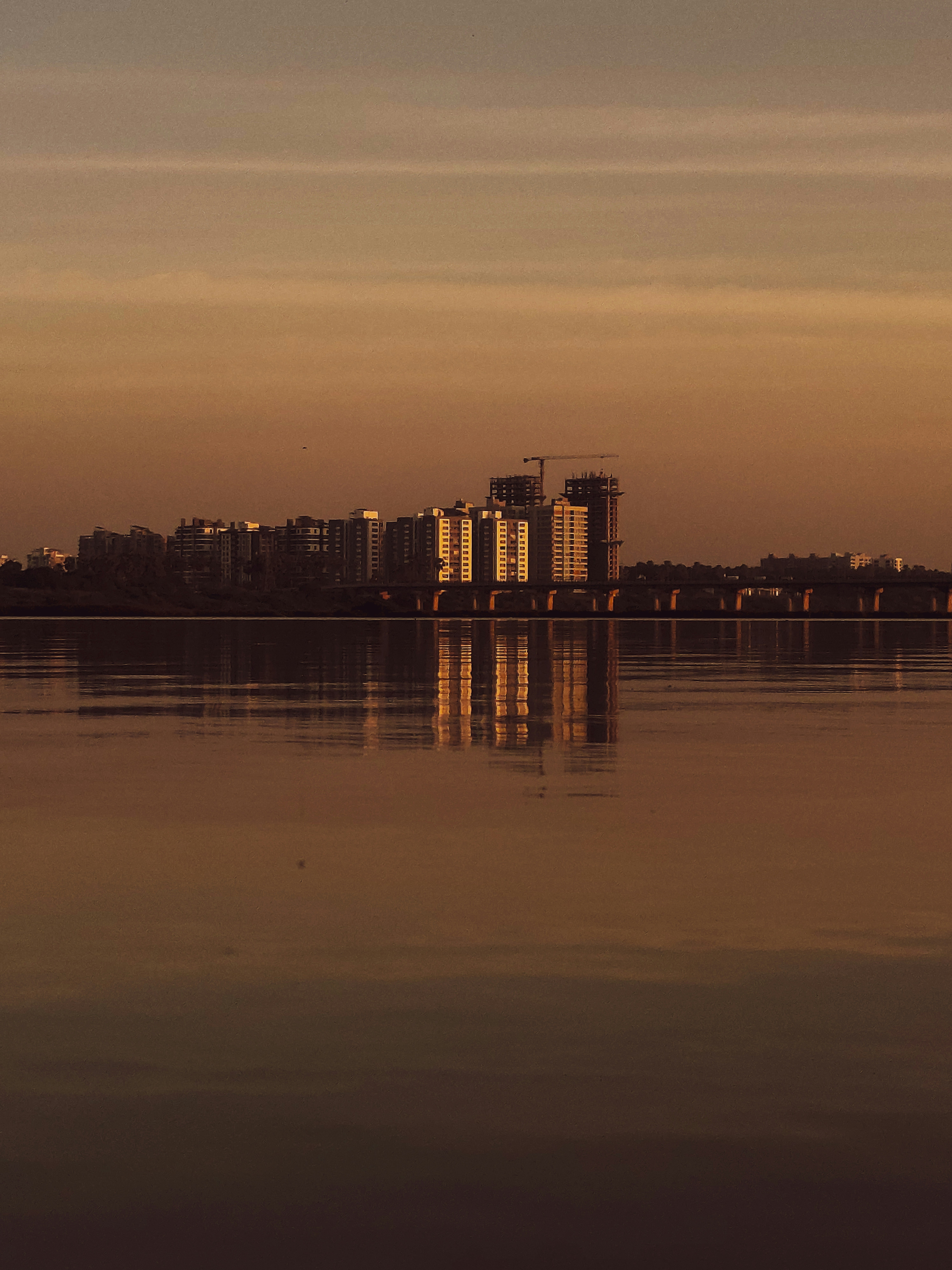 City skyline reflected on calm river at sunset with a soft golden hue.