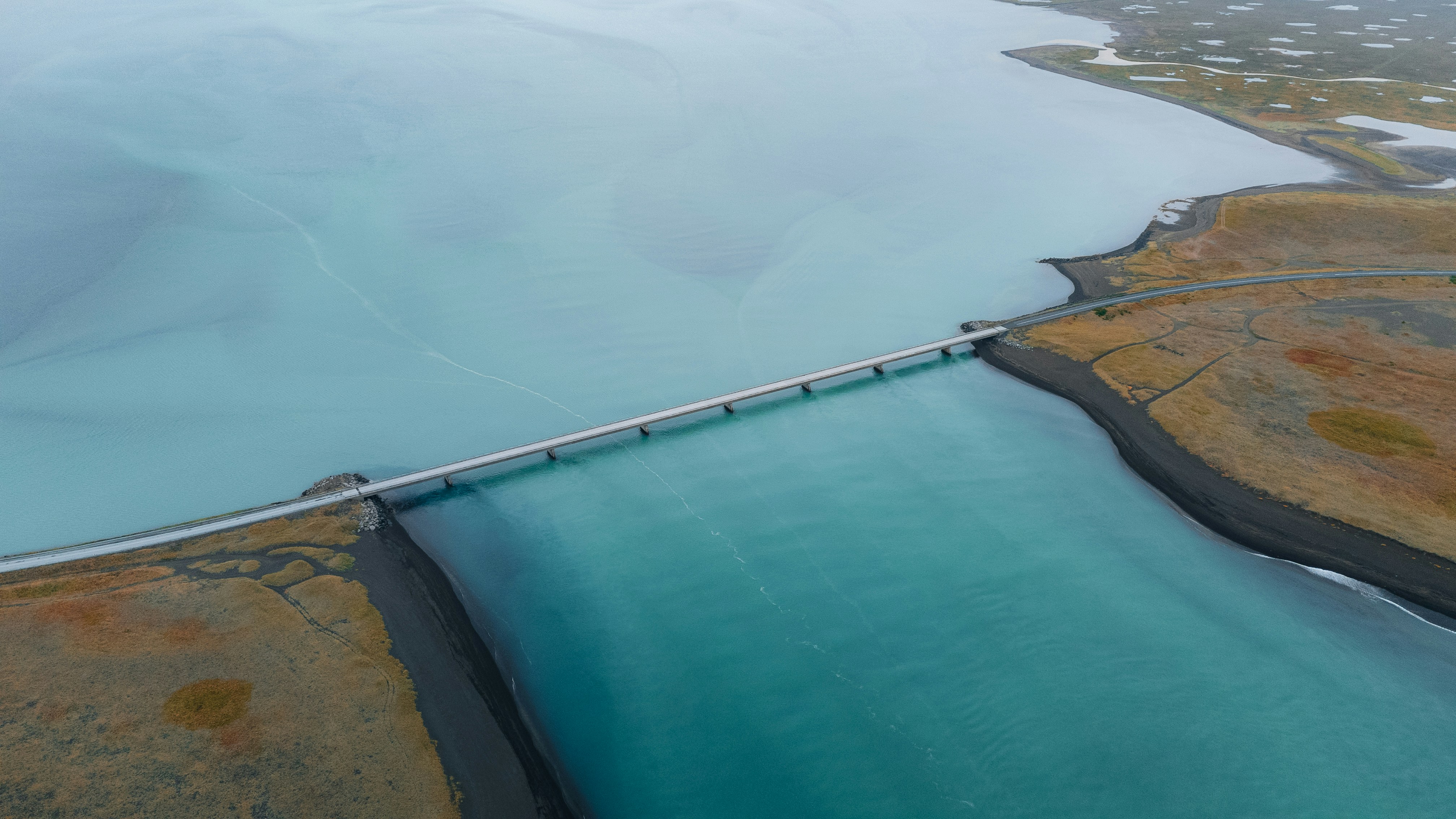 Aerial view of a long bridge spanning turquoise waters and barren landscapes.