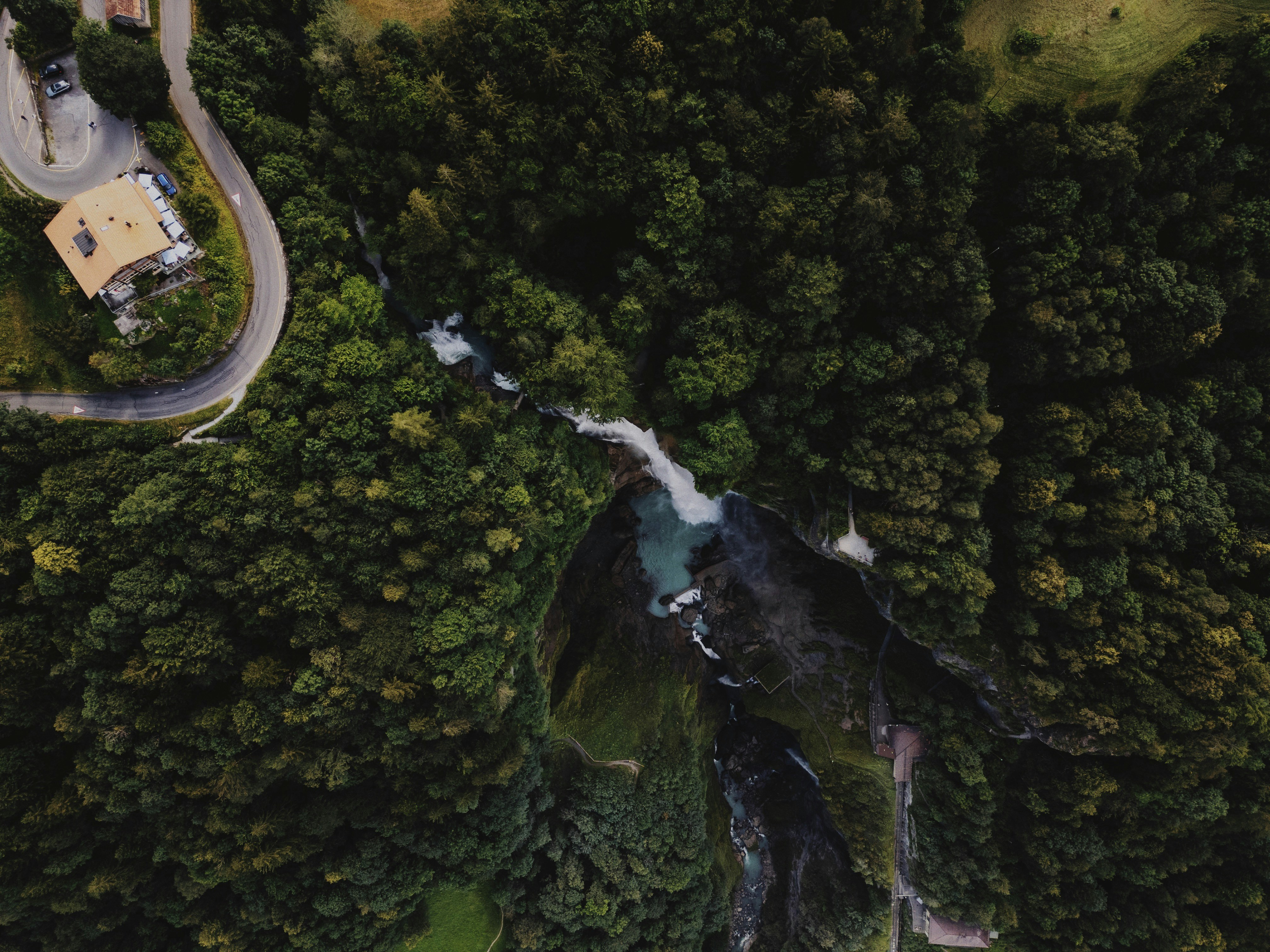 Aerial view of a waterfall cutting through dense green forest near a winding road.