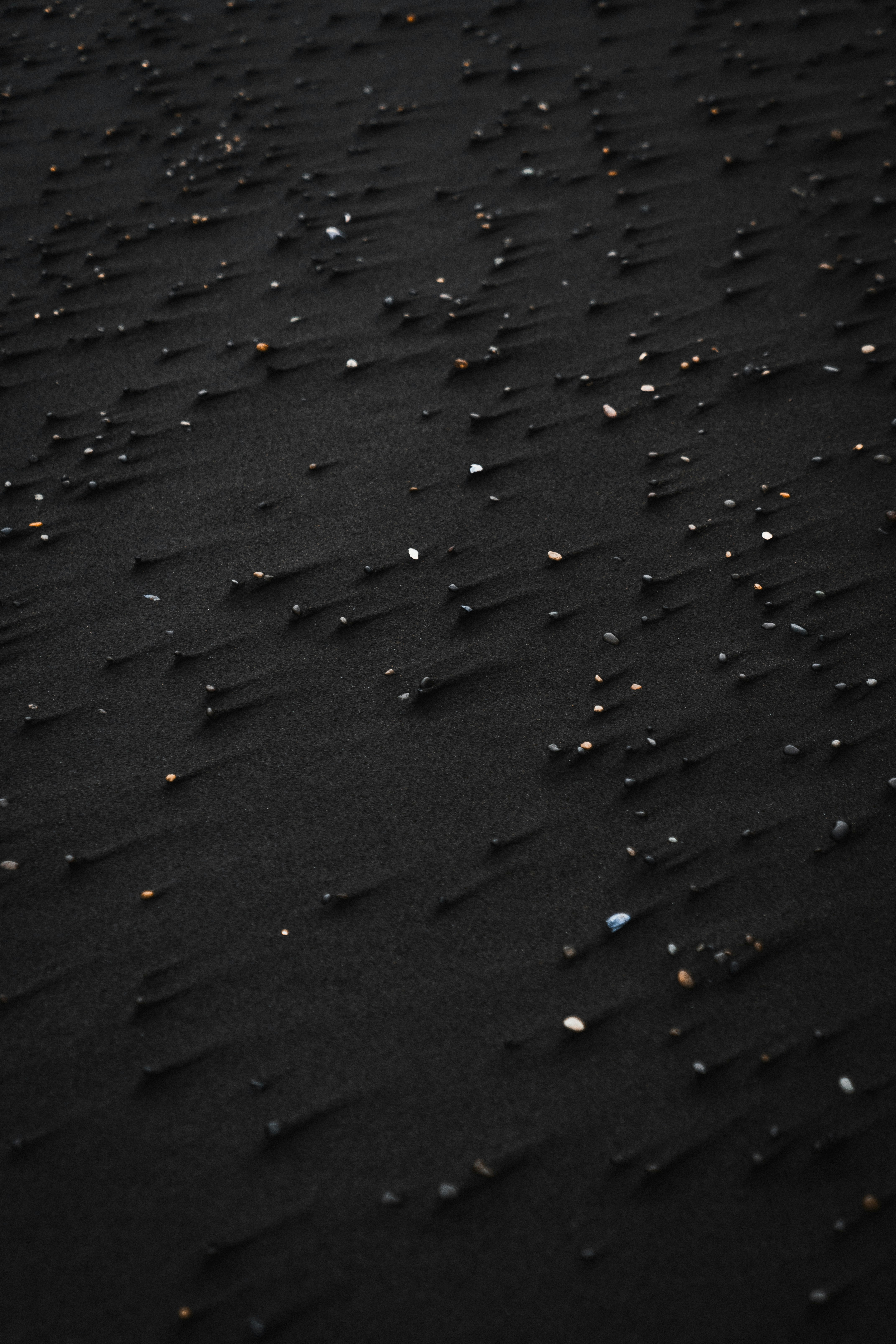 Small pebbles scattered across dark sand, forming abstract patterns.