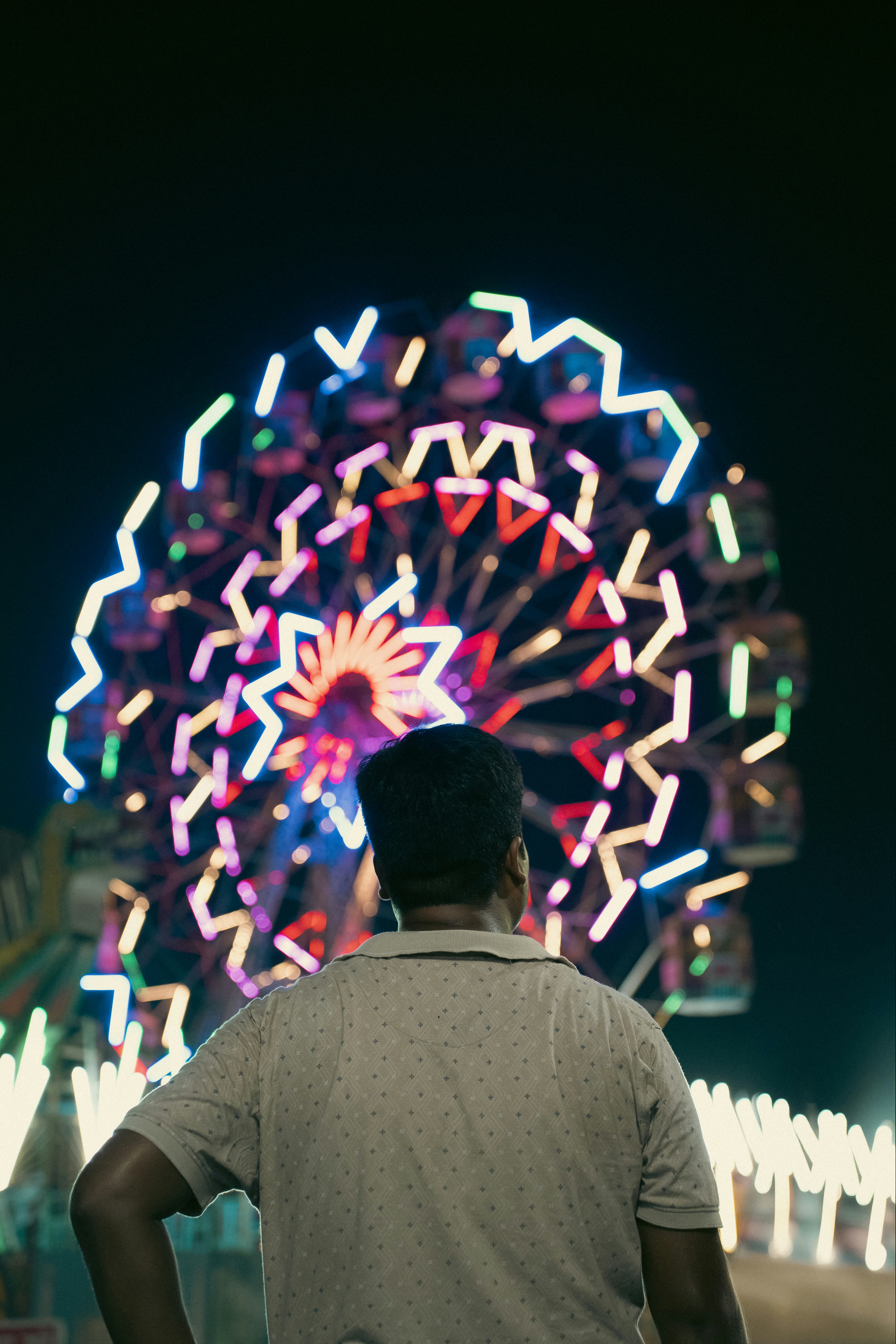 Neon Carousel Gaze: Back of a Visitor Before the Ferris Wheel