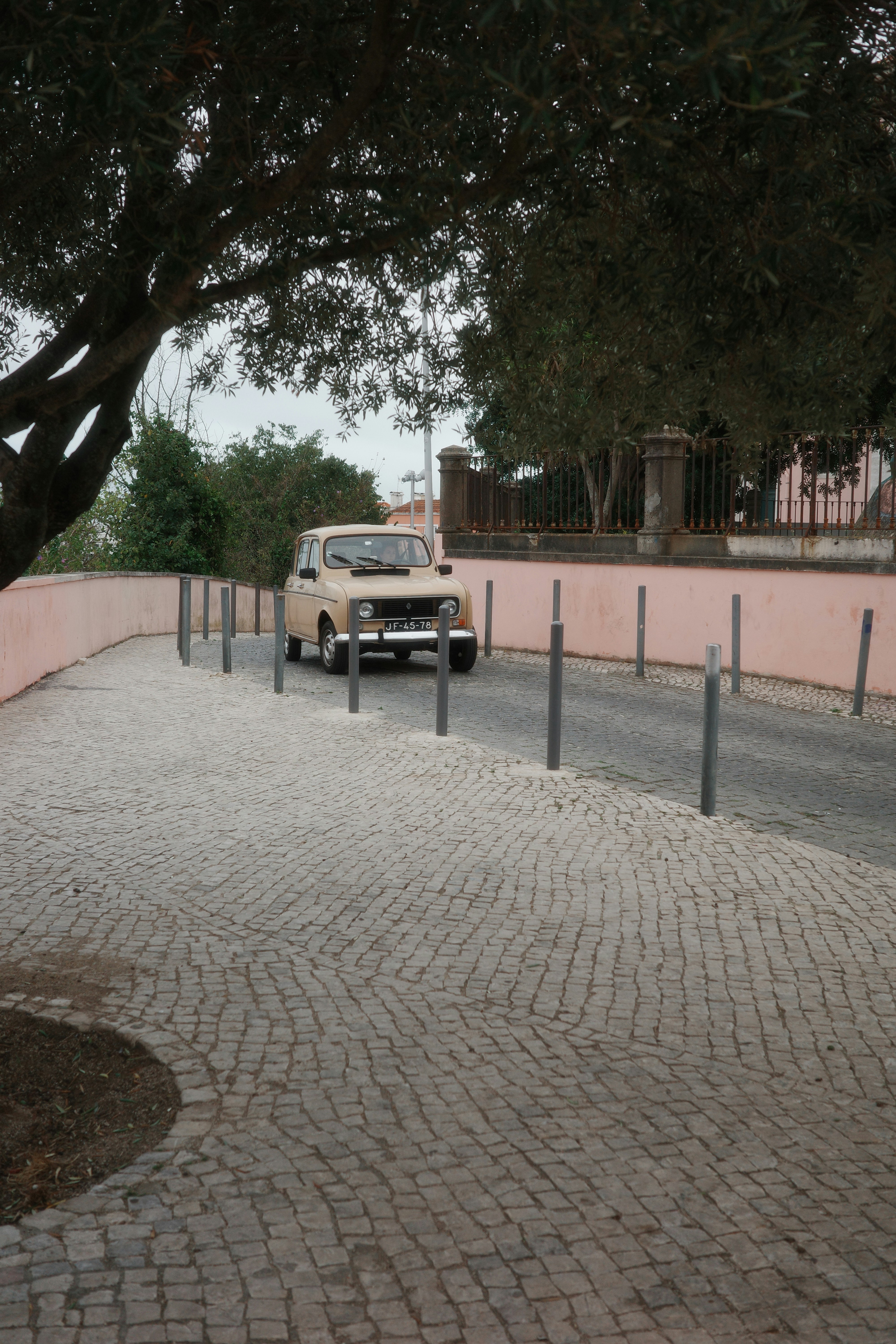 A classic vintage car makes its way down a peaceful cobblestone street in Lisbon, Portugal, framed by a large tree and pastel walls. The scene captures the timeless charm of Lisbon’s quieter streets, blending retro elements with the city’s historic and scenic beauty. This picturesque moment invites viewers to step back in time and appreciate the slower pace of life in Portugal’s capital.