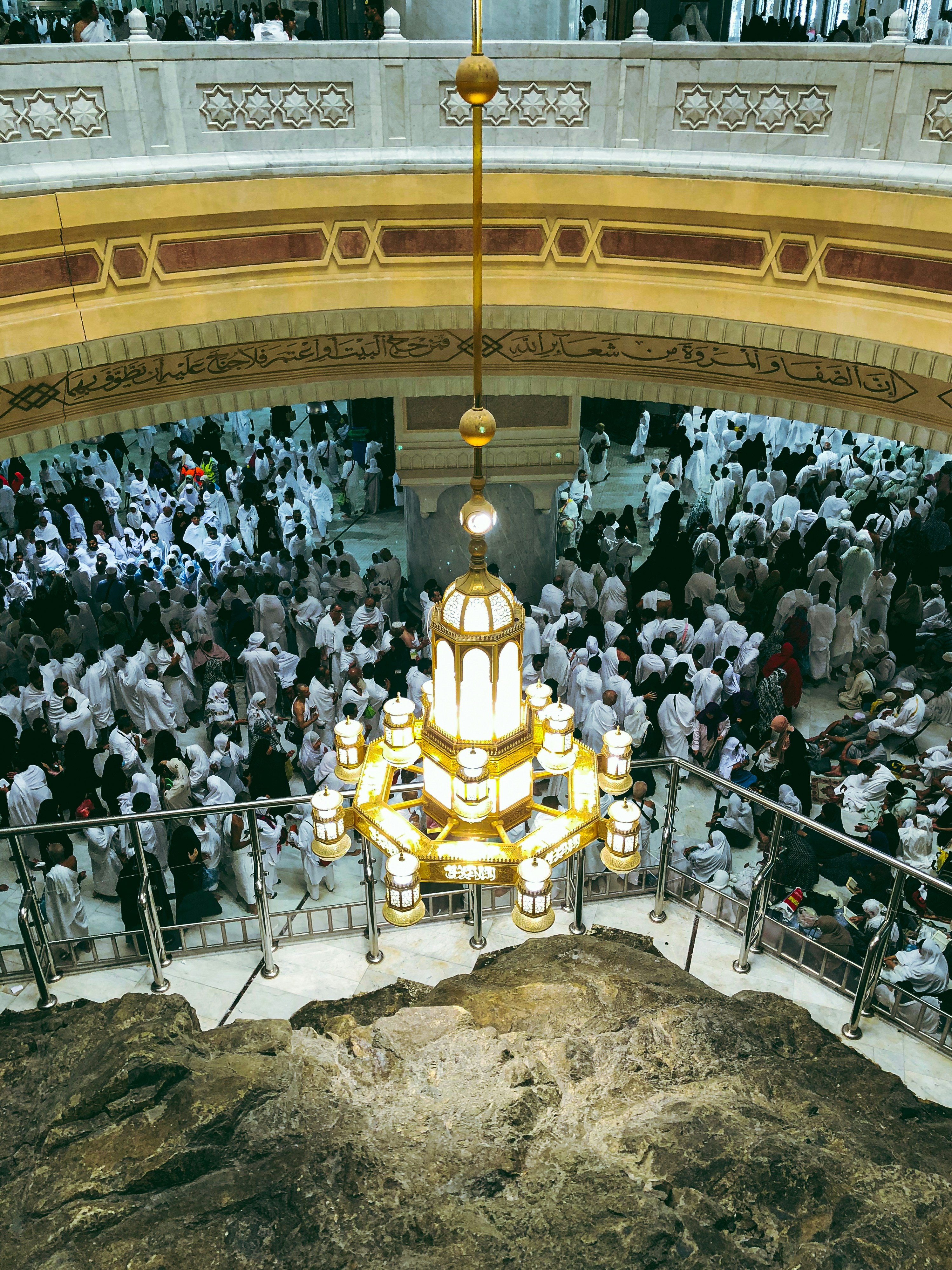 A gilded lantern suspended over a circular marble courtyard, surrounded by a dense crowd in white garments.