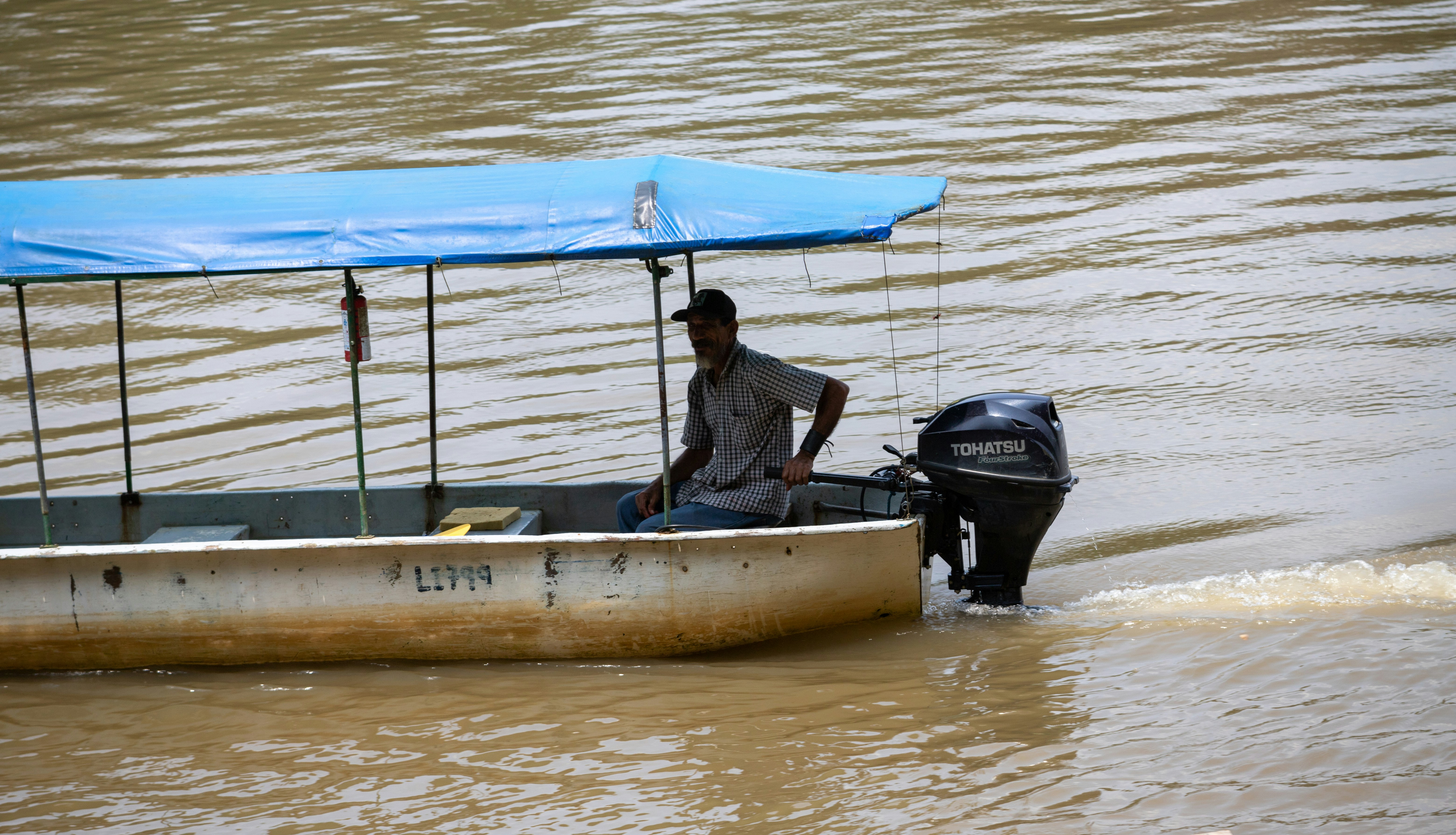 Blue Canopy over Murky Waters: A Solo Boatman Navigates the River