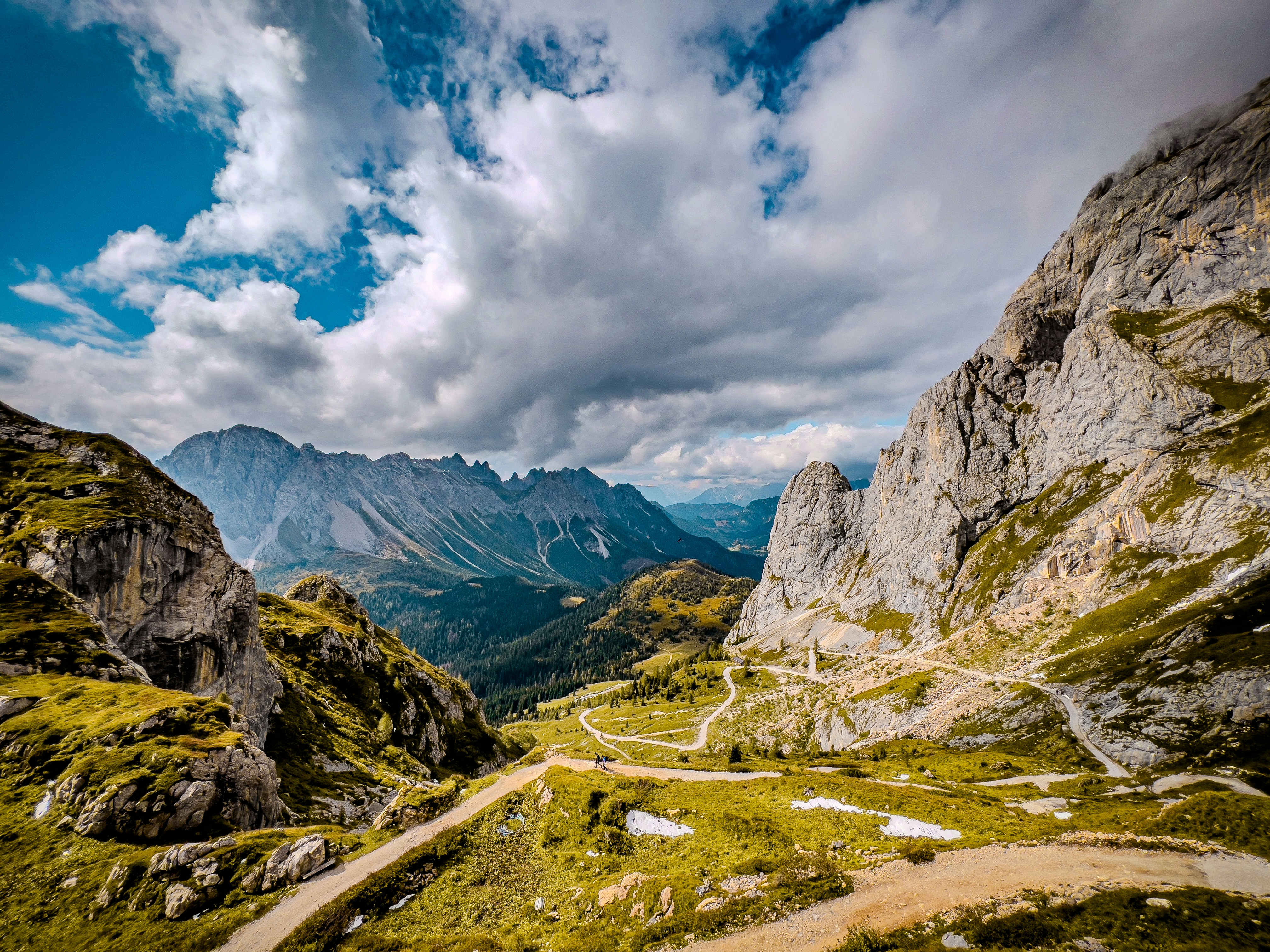 Winding road traversing rocky mountains under a dynamic cloud-filled sky.