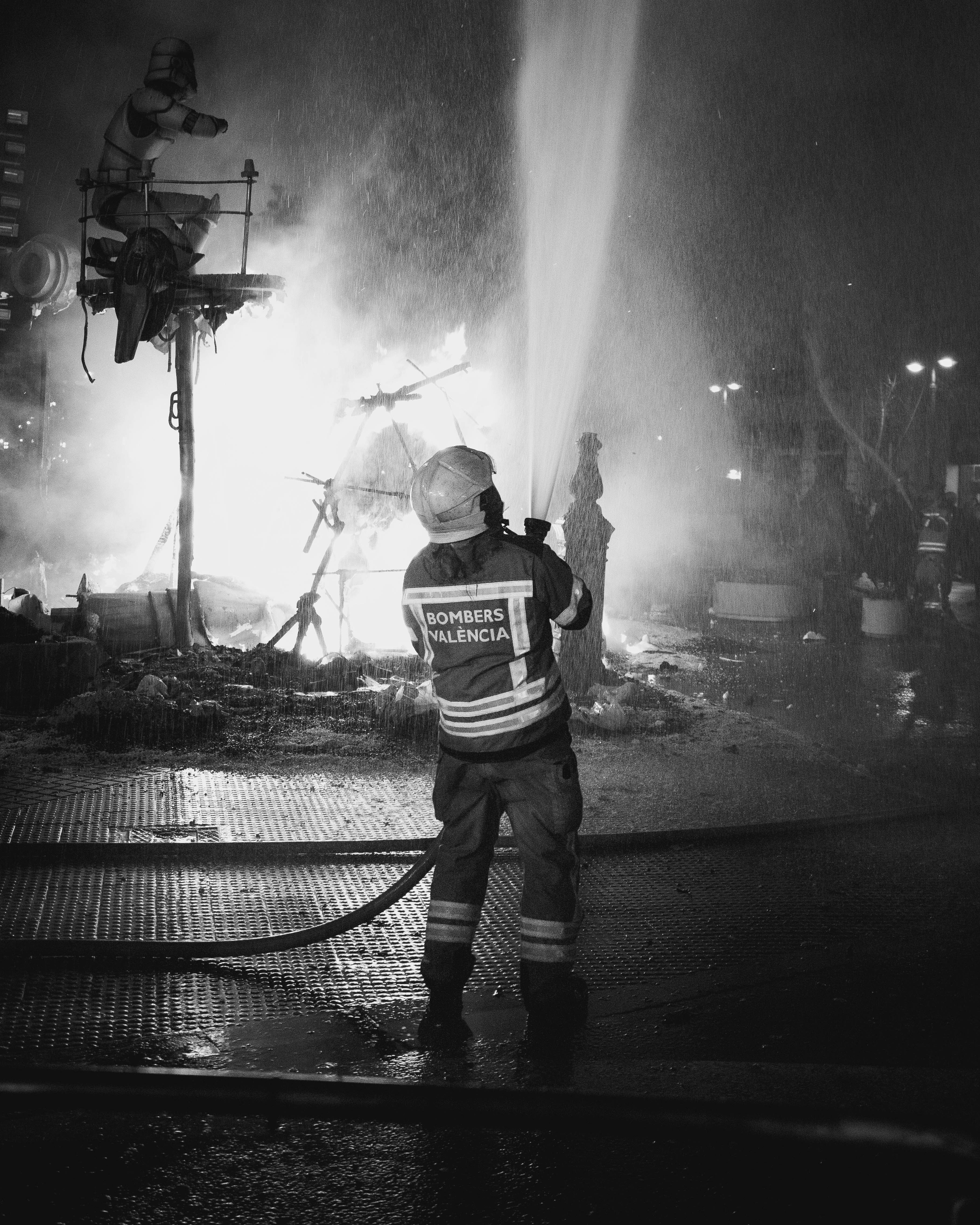 A fireman standing in front of a fire with a hose photo – Free ...