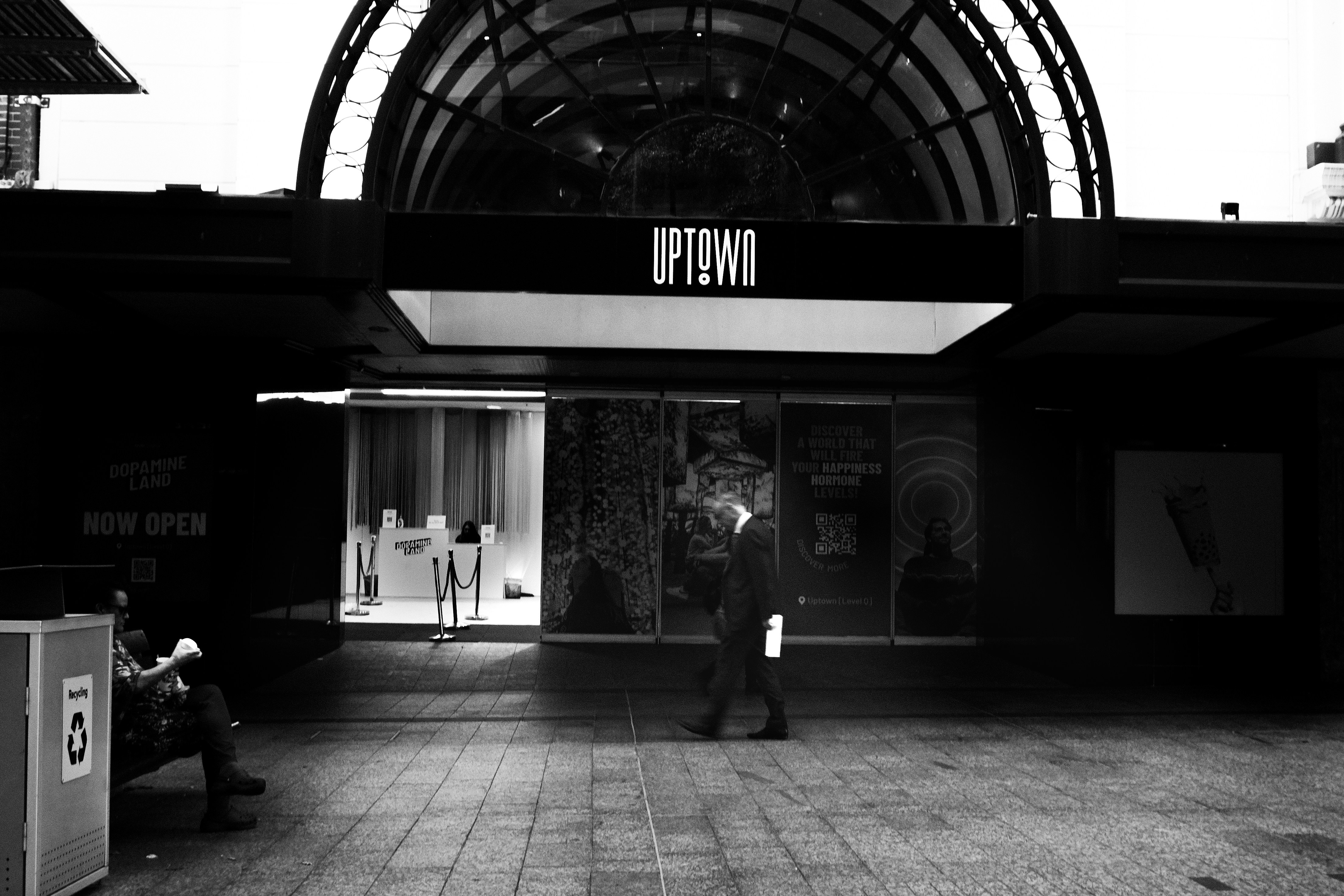 Crossing the Uptown Arch: A solitary figure walks beneath a quiet storefront