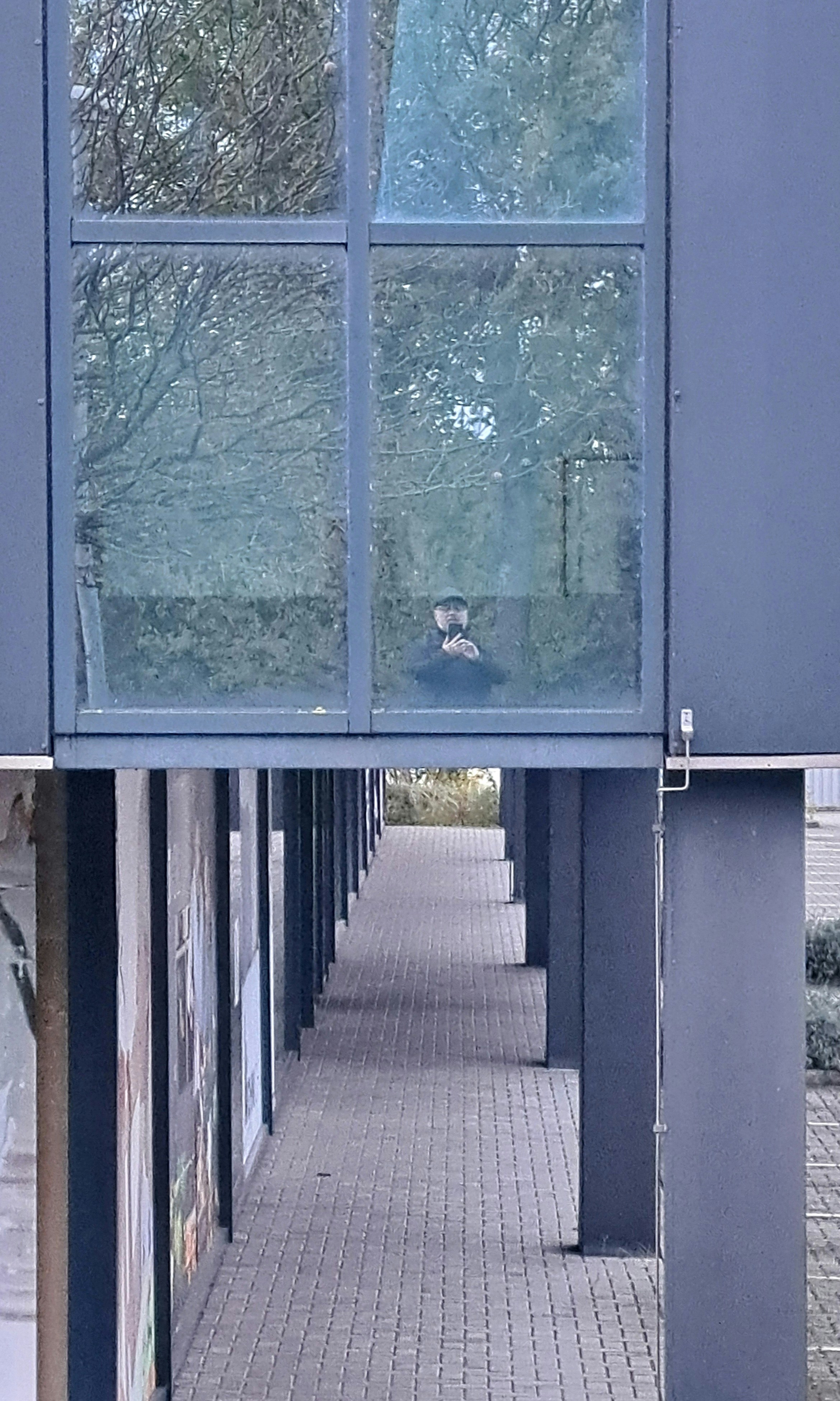 Glass Corridor Reflection: The Photographer Revealed in Blue Frames
