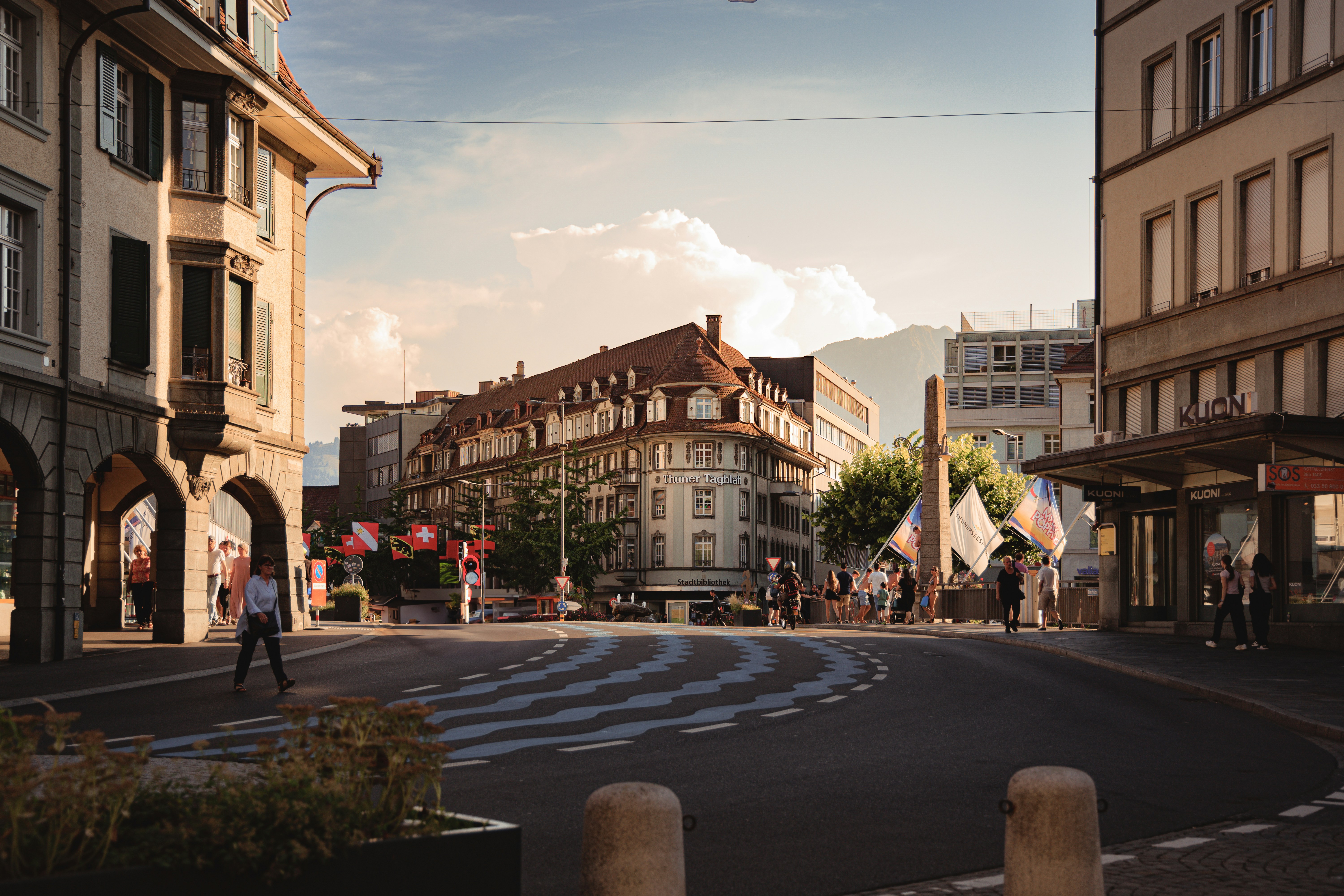People walking through a sunlit urban intersection surrounded by historic European architecture.