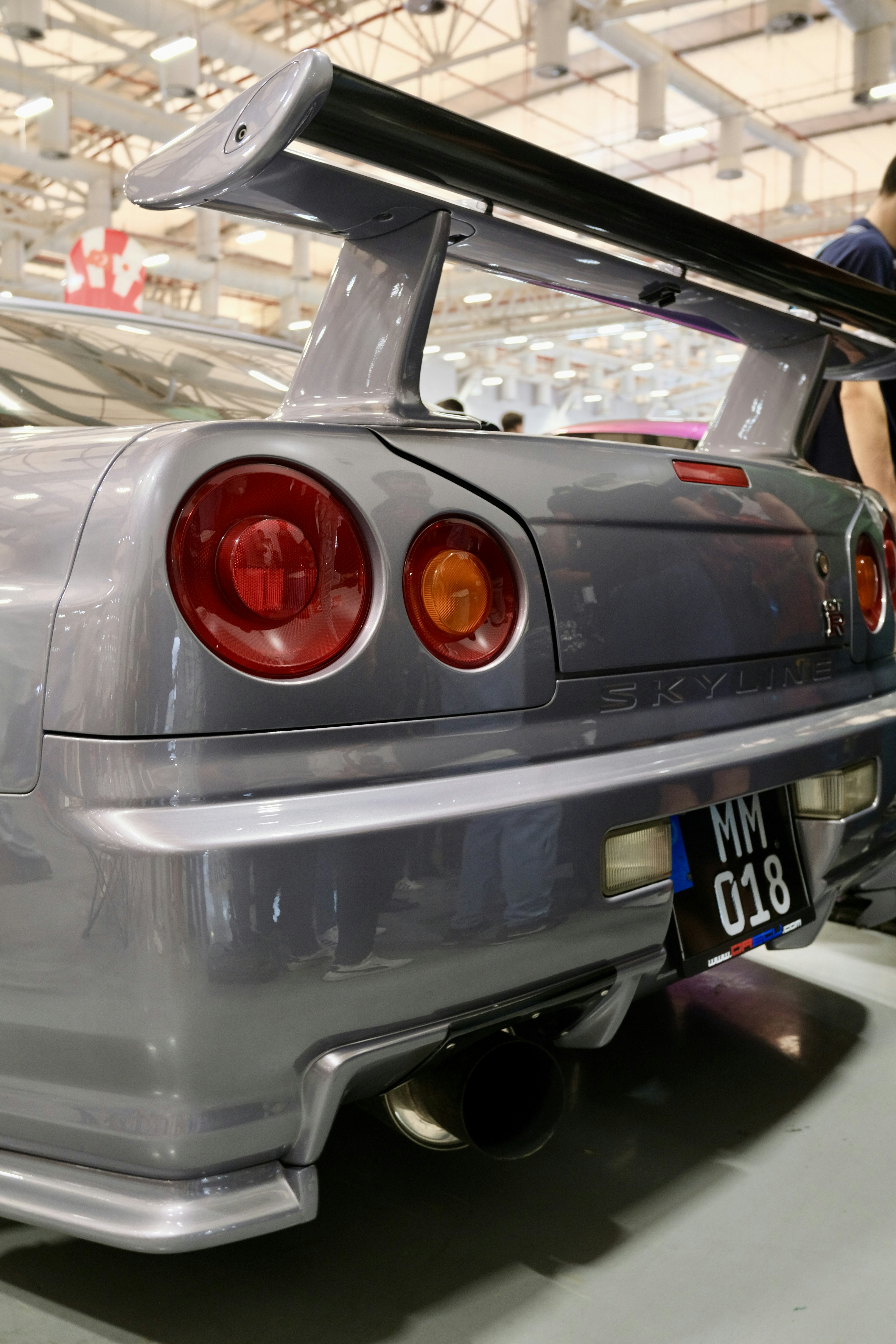 Close-up of a silver sports car's rear, showcasing its aerodynamic spoiler and circular taillights in a well-lit garage.