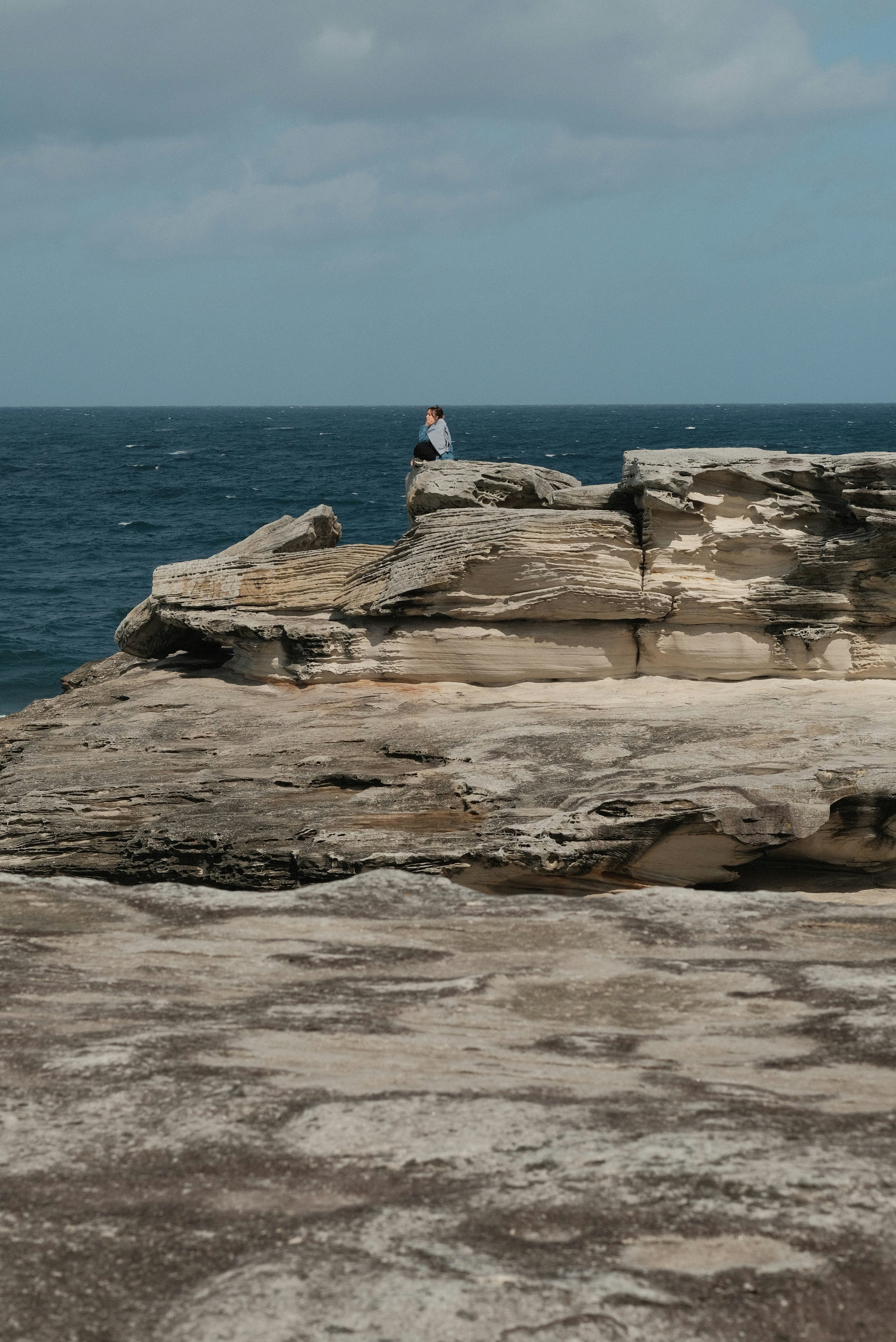 A solitary figure perched on wind-worn coastal ledge against the open sea