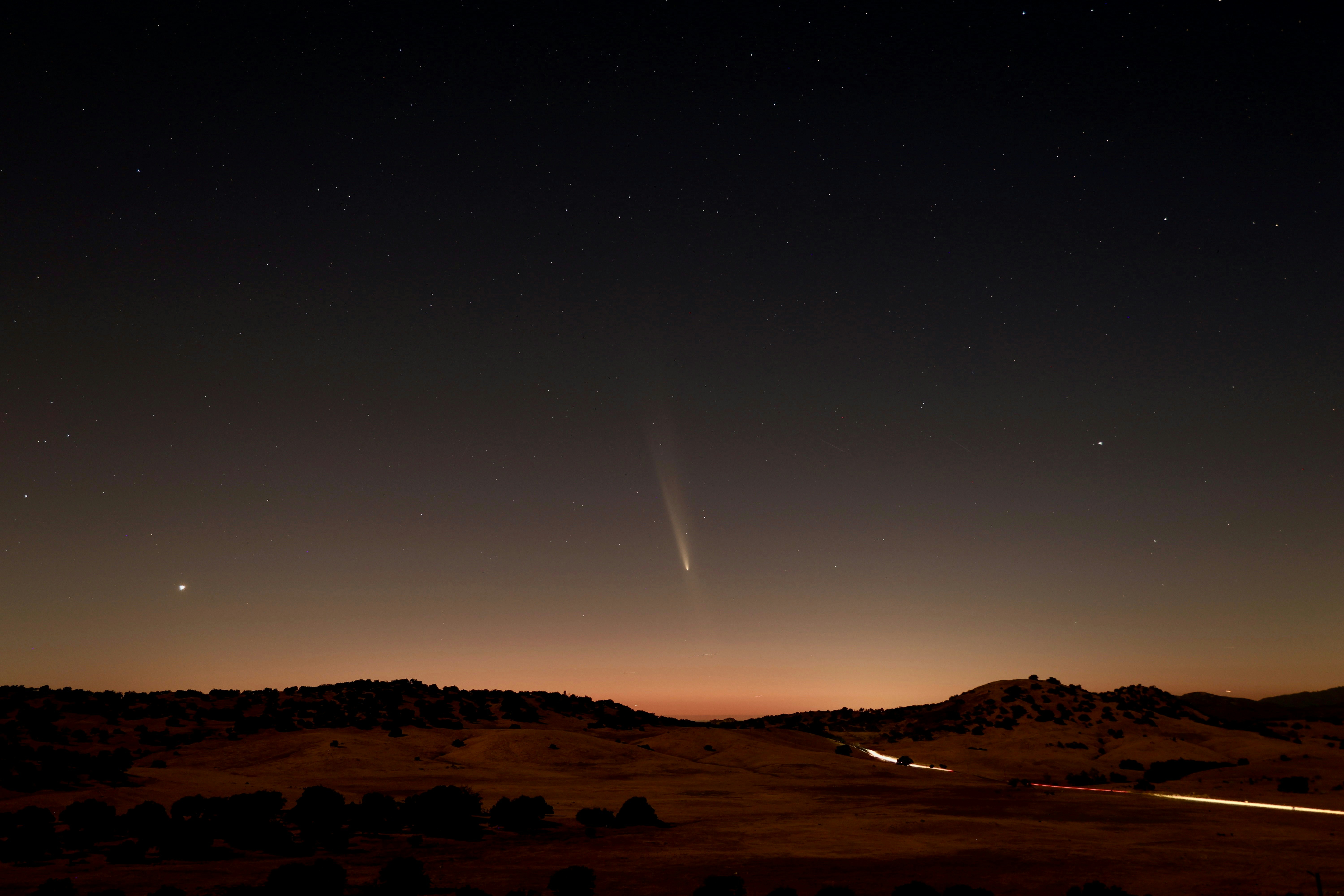 Comet streaks across a starry sky above a tranquil landscape at dusk.